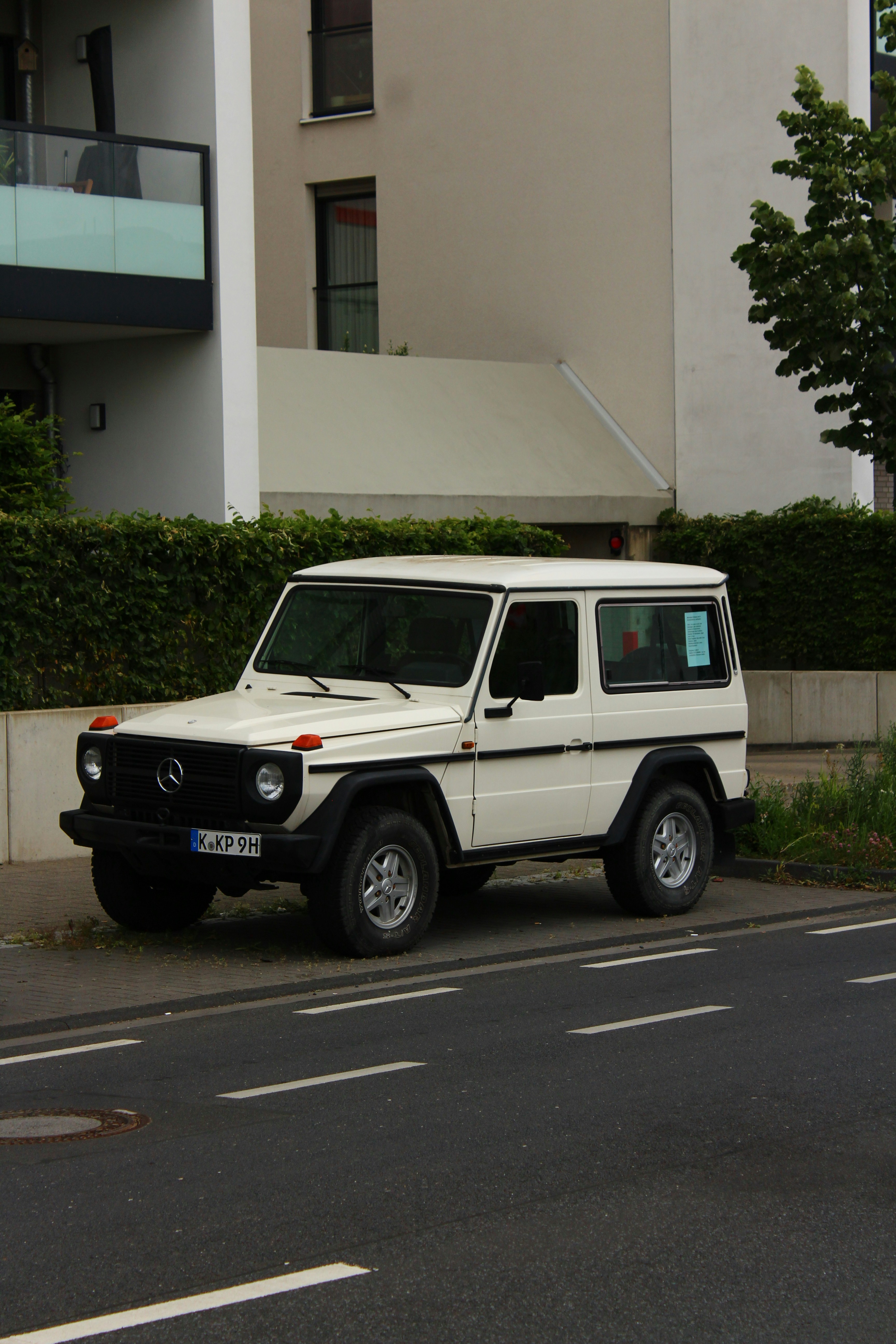 White G-Class Parks on a Quiet Street by a Minimalist Modern Building