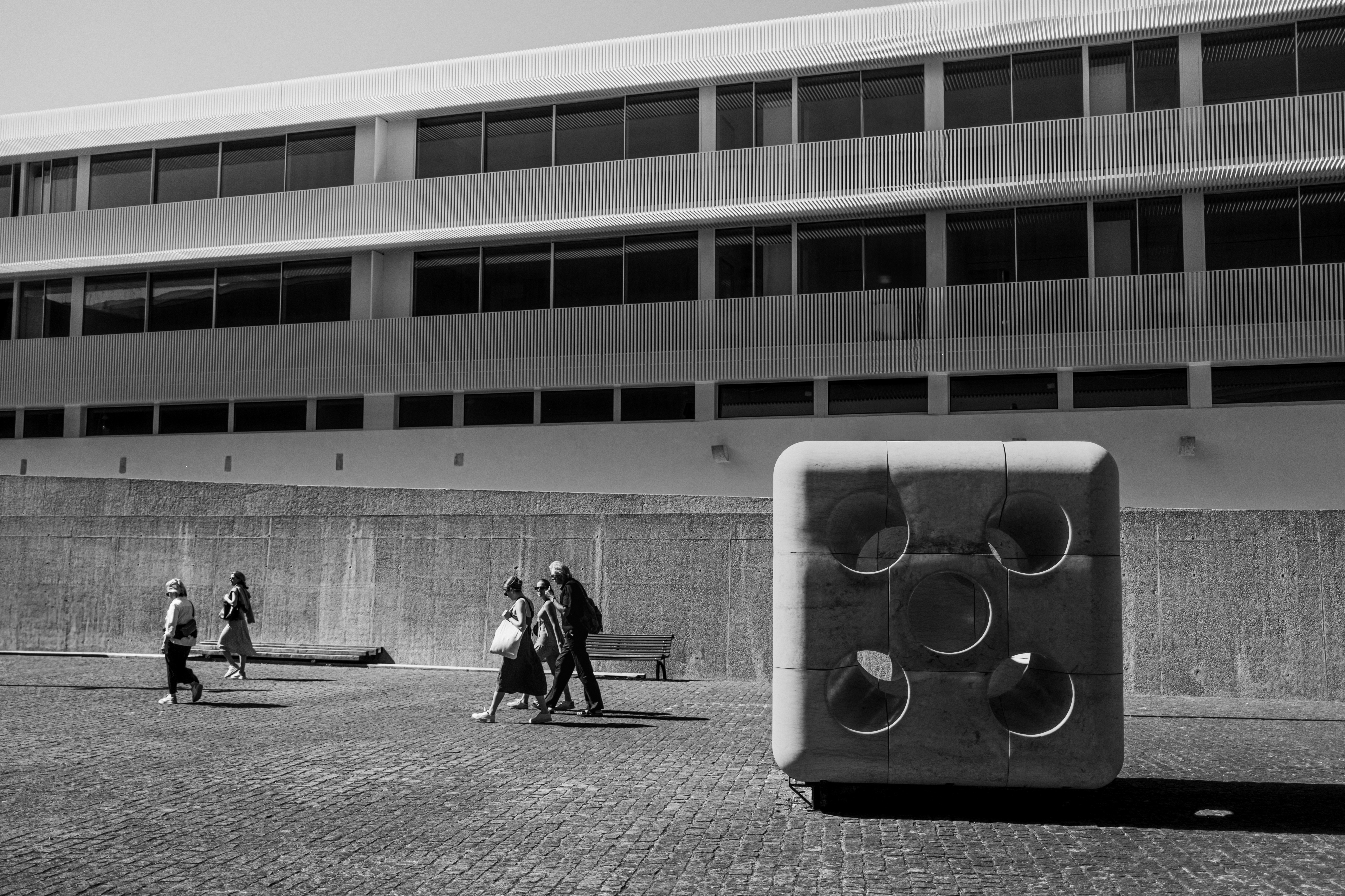 People walk past a sculpture near a building. photo – Free Street ...