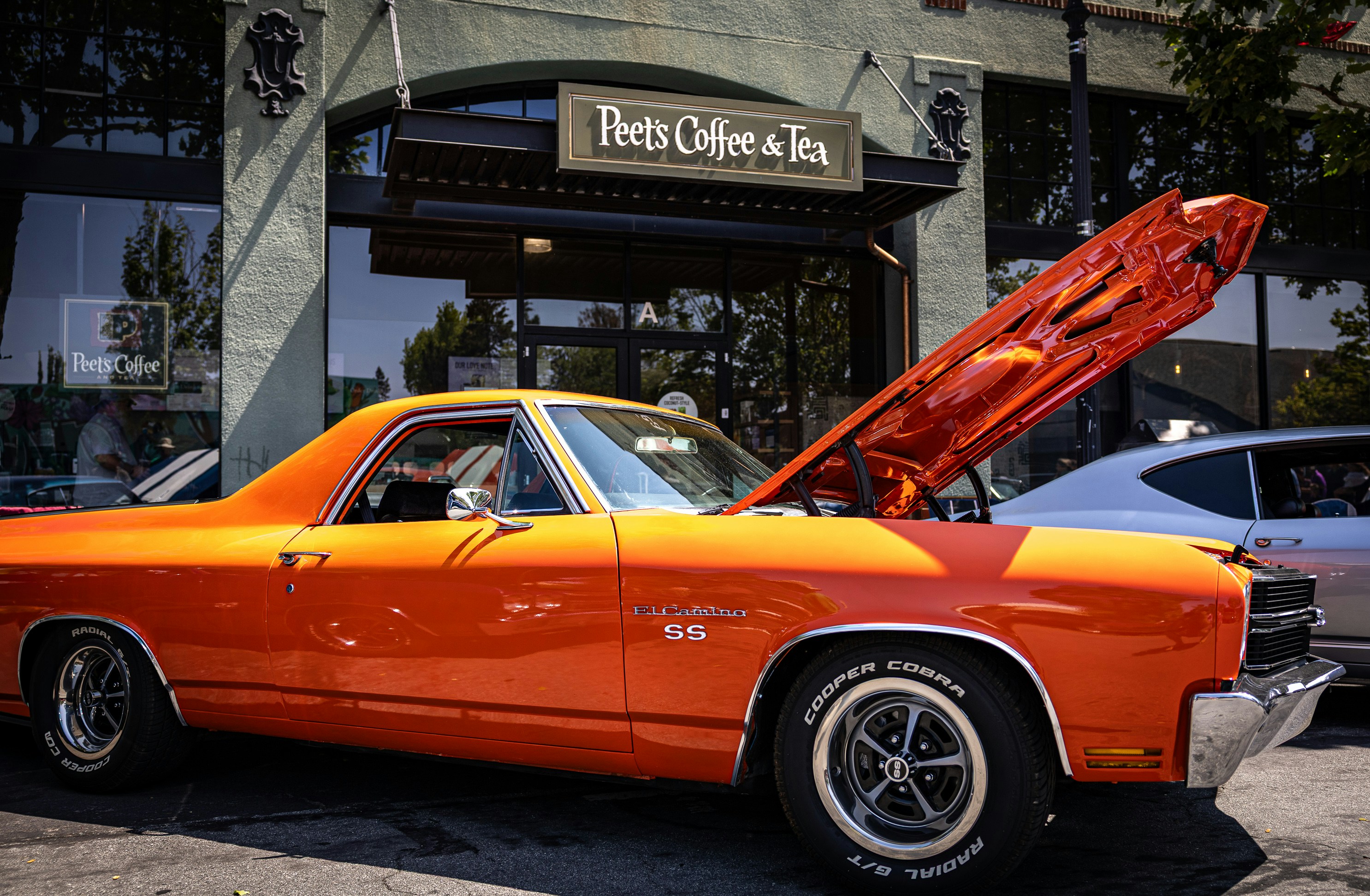 Classic orange Chevrolet El Camino parked outside Peet's Coffee & Tea, showcasing its open hood and vintage detailing.