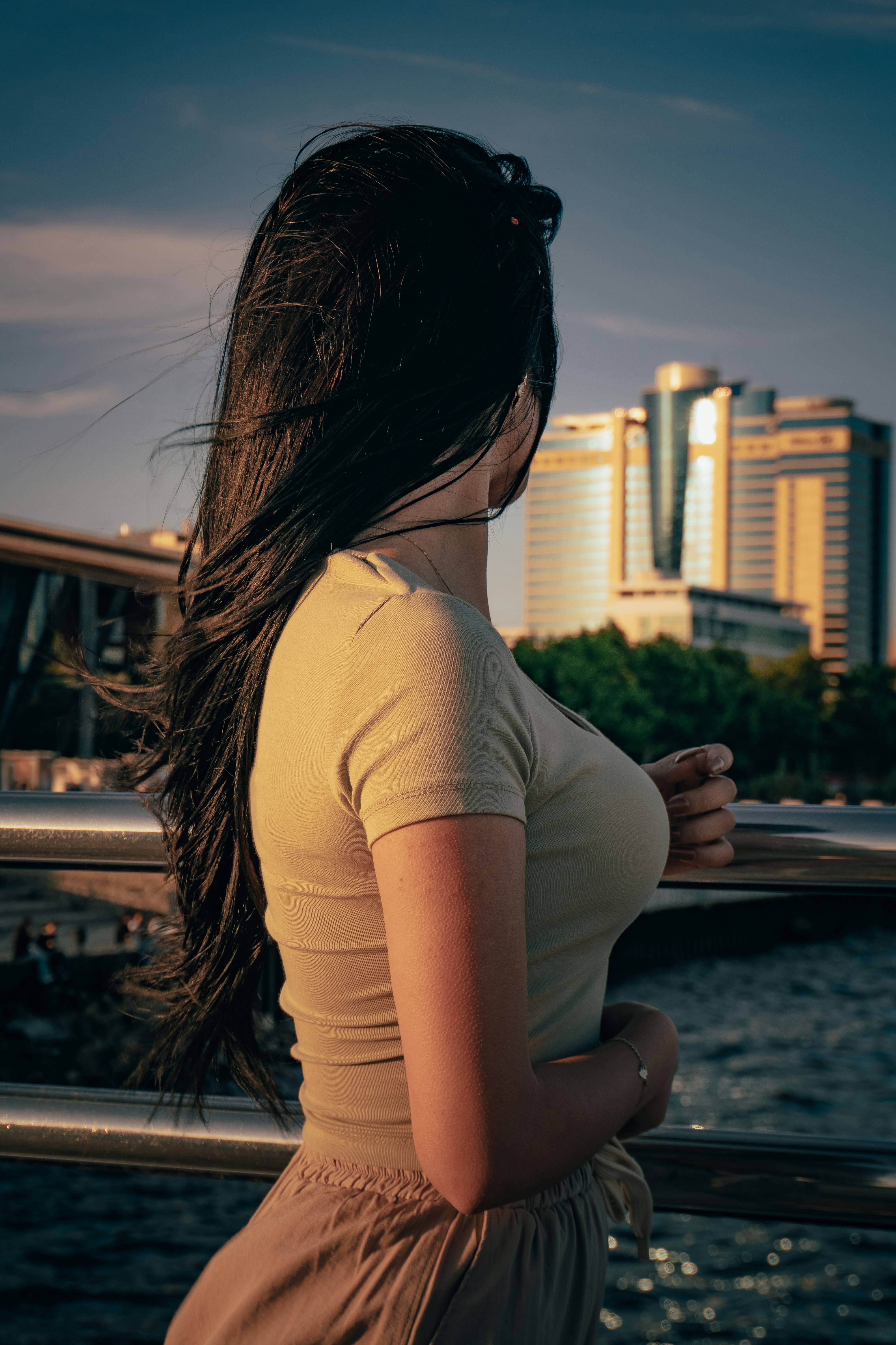 Riverfront Reverie: Beige-clad Figure Framed by Golden City Lights