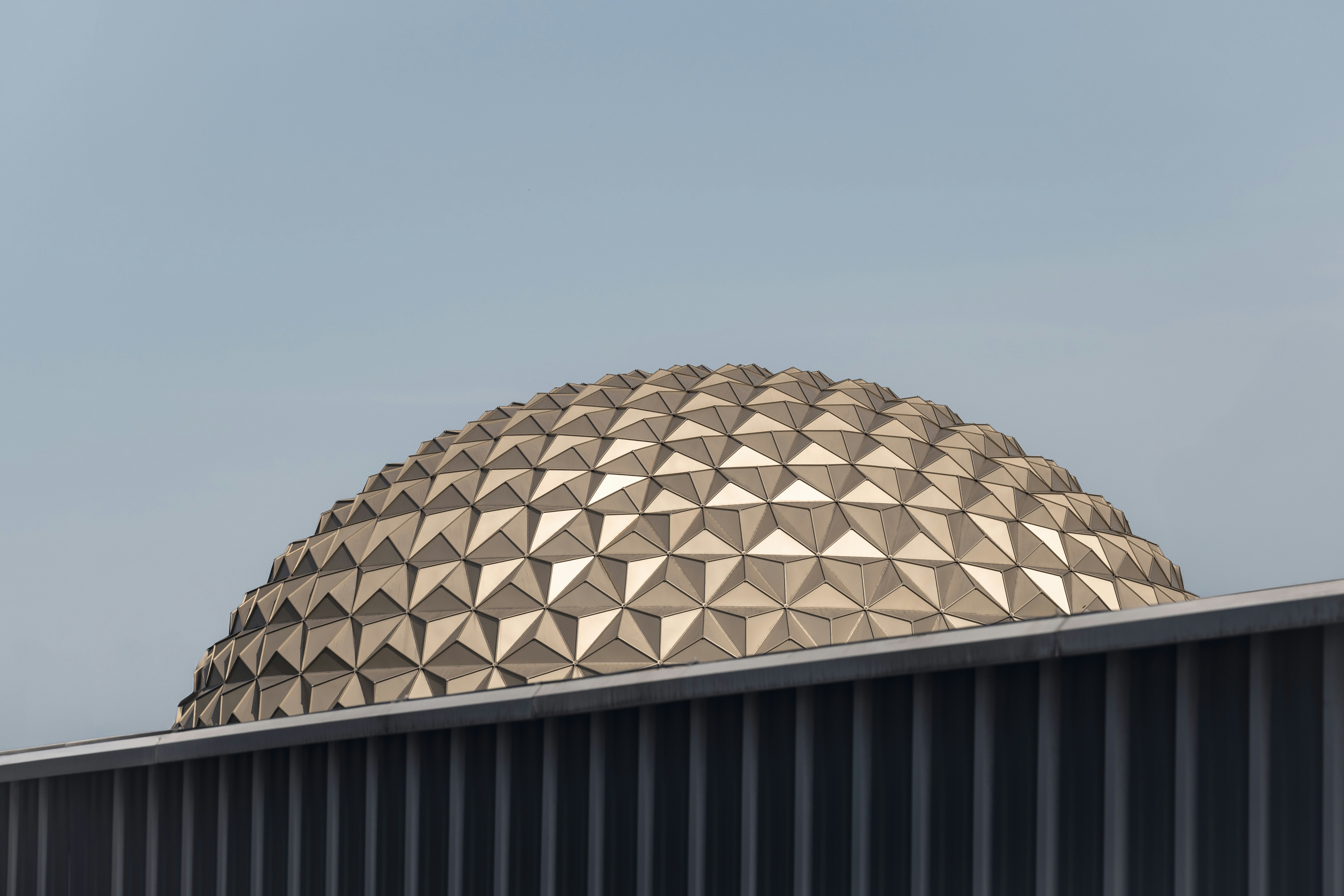 A geometric dome with intricate triangular facets stands against a clear sky, showcasing modern architectural design.