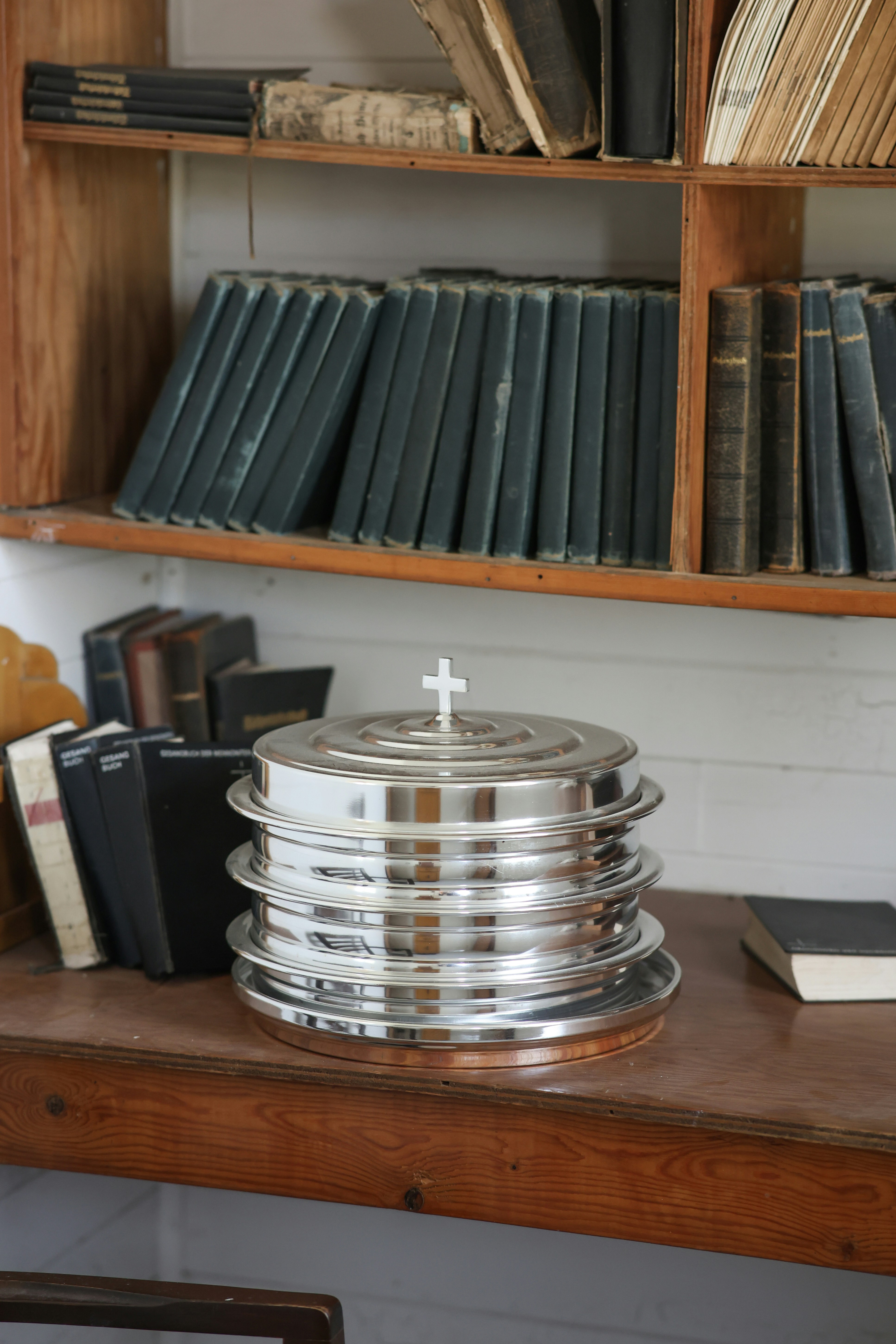 Tiered Silver Relic Crowned with a Cross, Resting Among Quiet Tomes