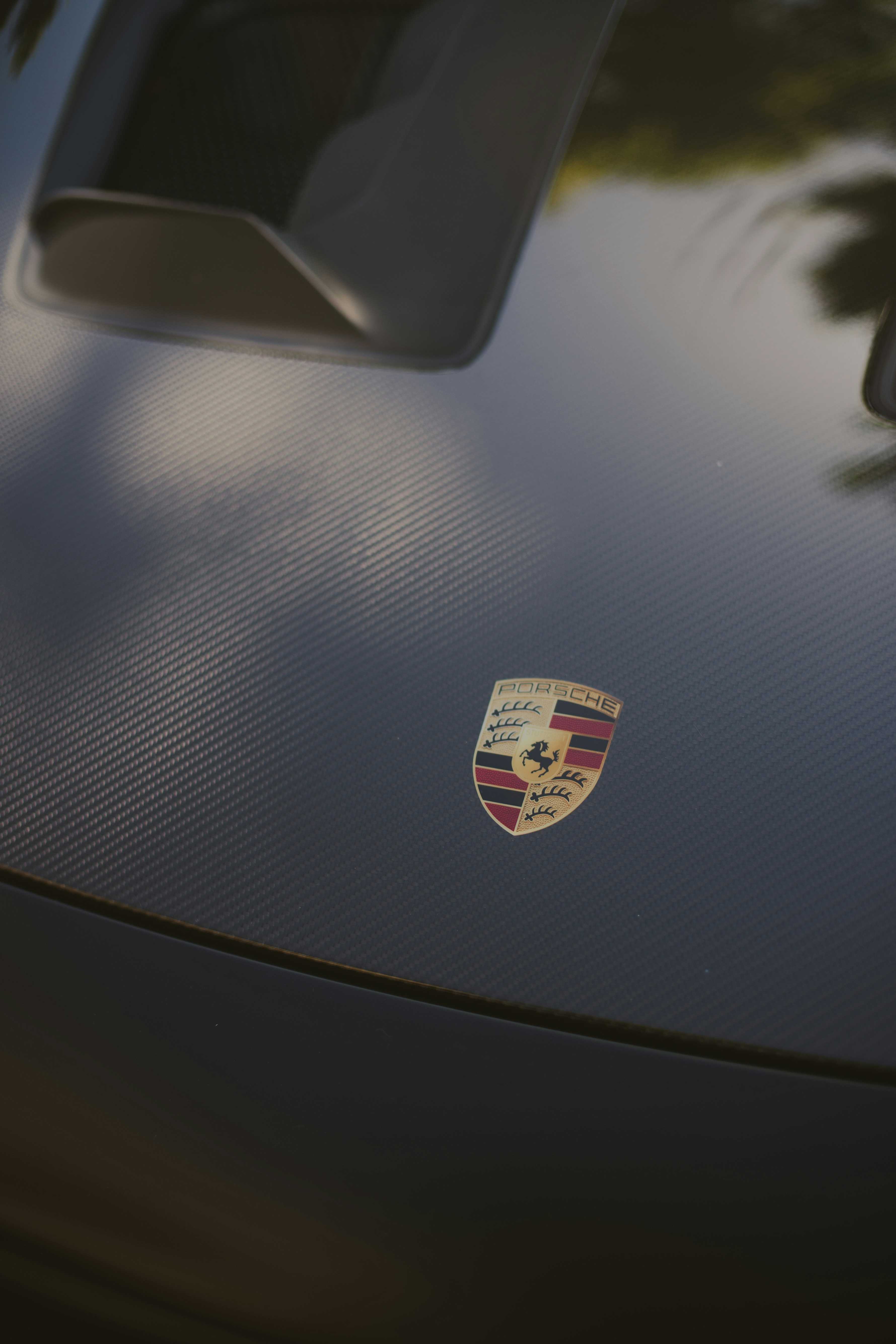Close-up of a Porsche logo on a sleek carbon fiber surface, highlighting the brand's luxury and performance heritage.