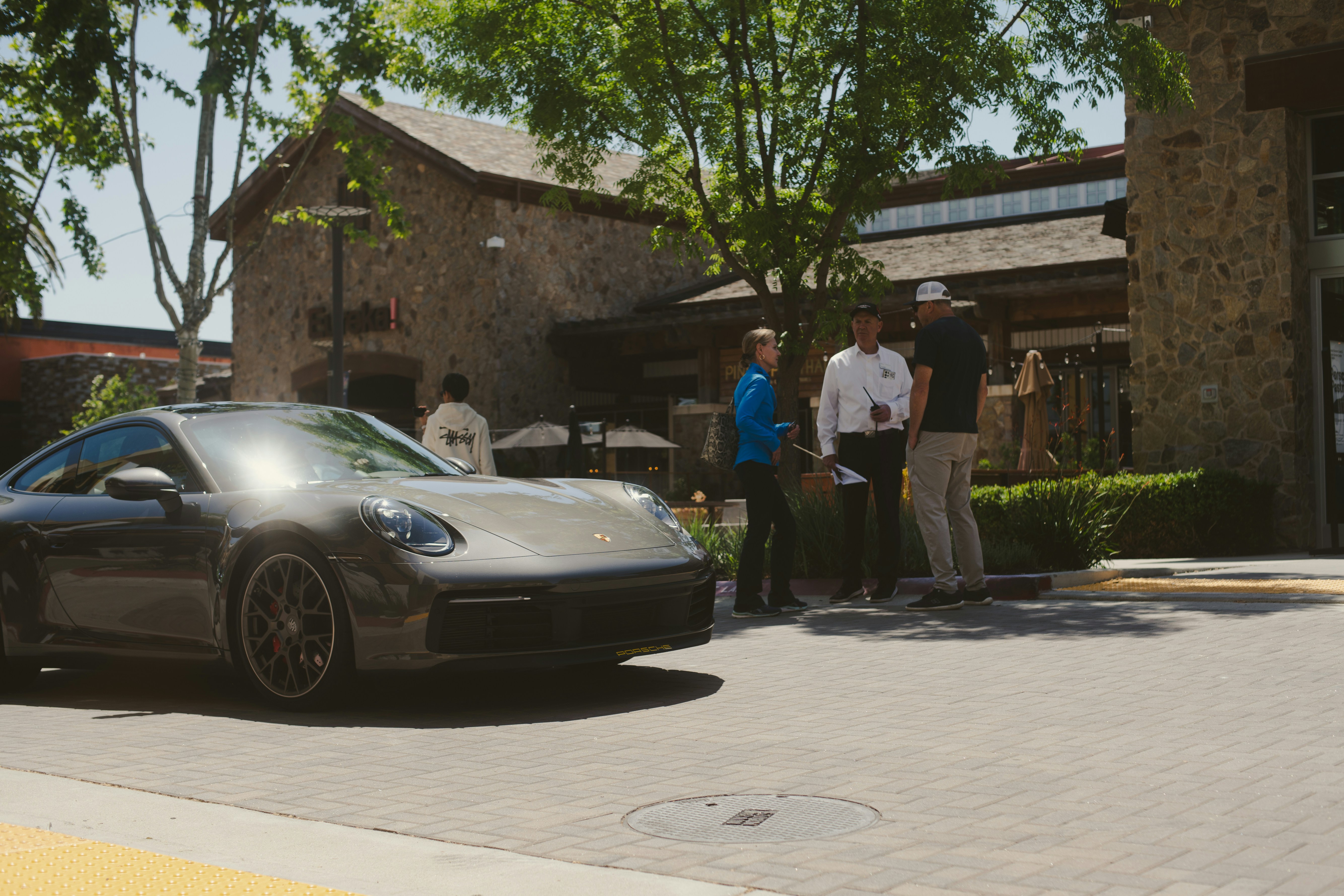 Midday Gray Porsche Anchors a Casual Car Meet in a Shaded Stone Courtyard