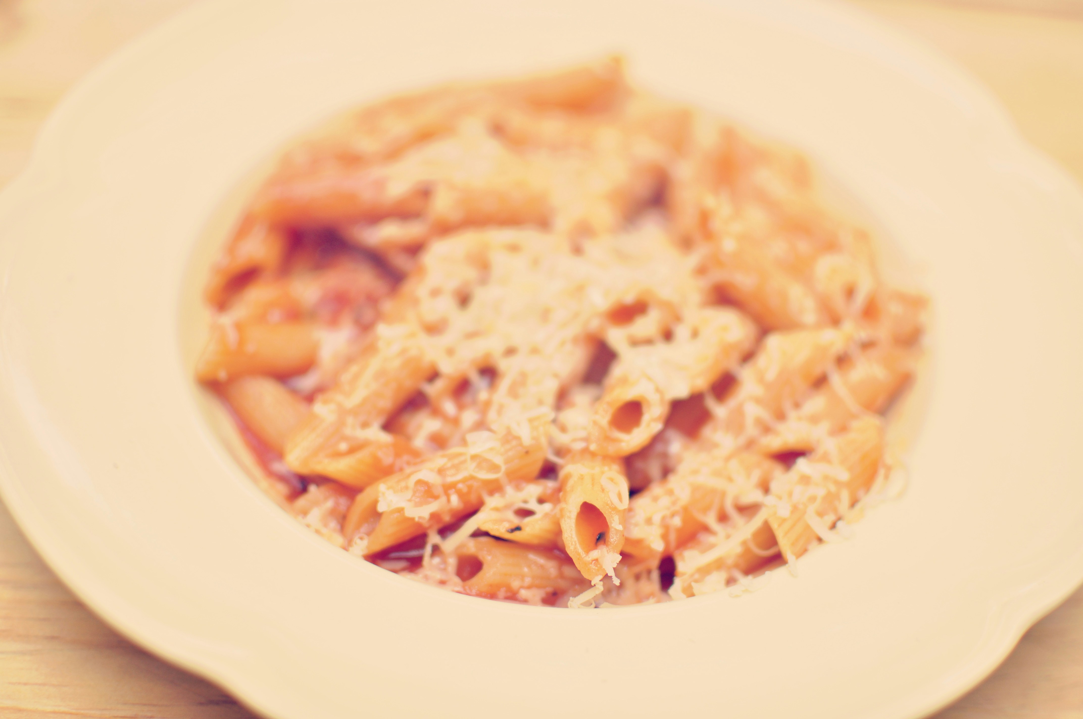 Pasta in a white bowl, topped with cheese.