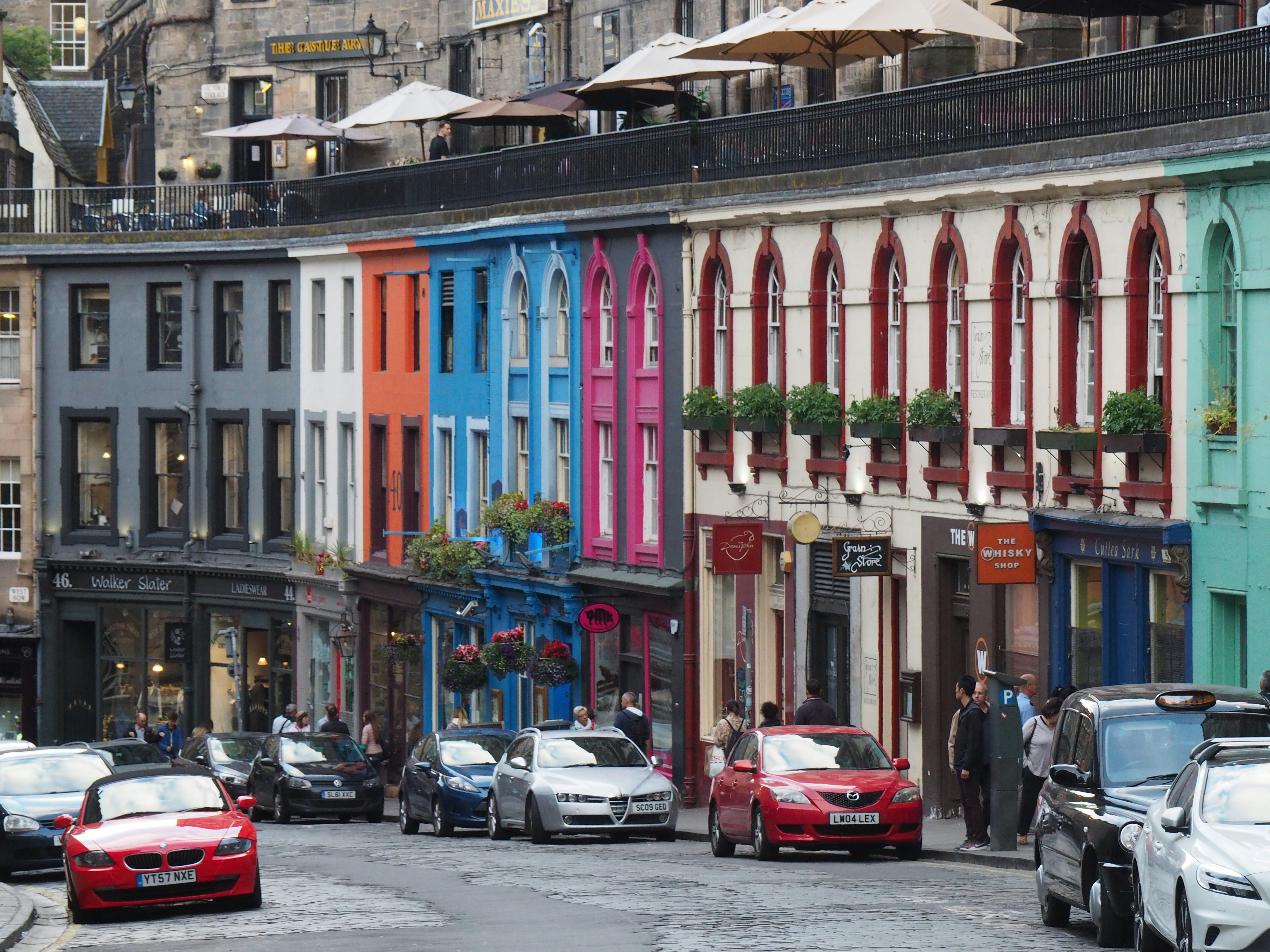 Colorful buildings lining a cobblestone street, showcasing a blend of shops and vehicles in a lively urban setting.