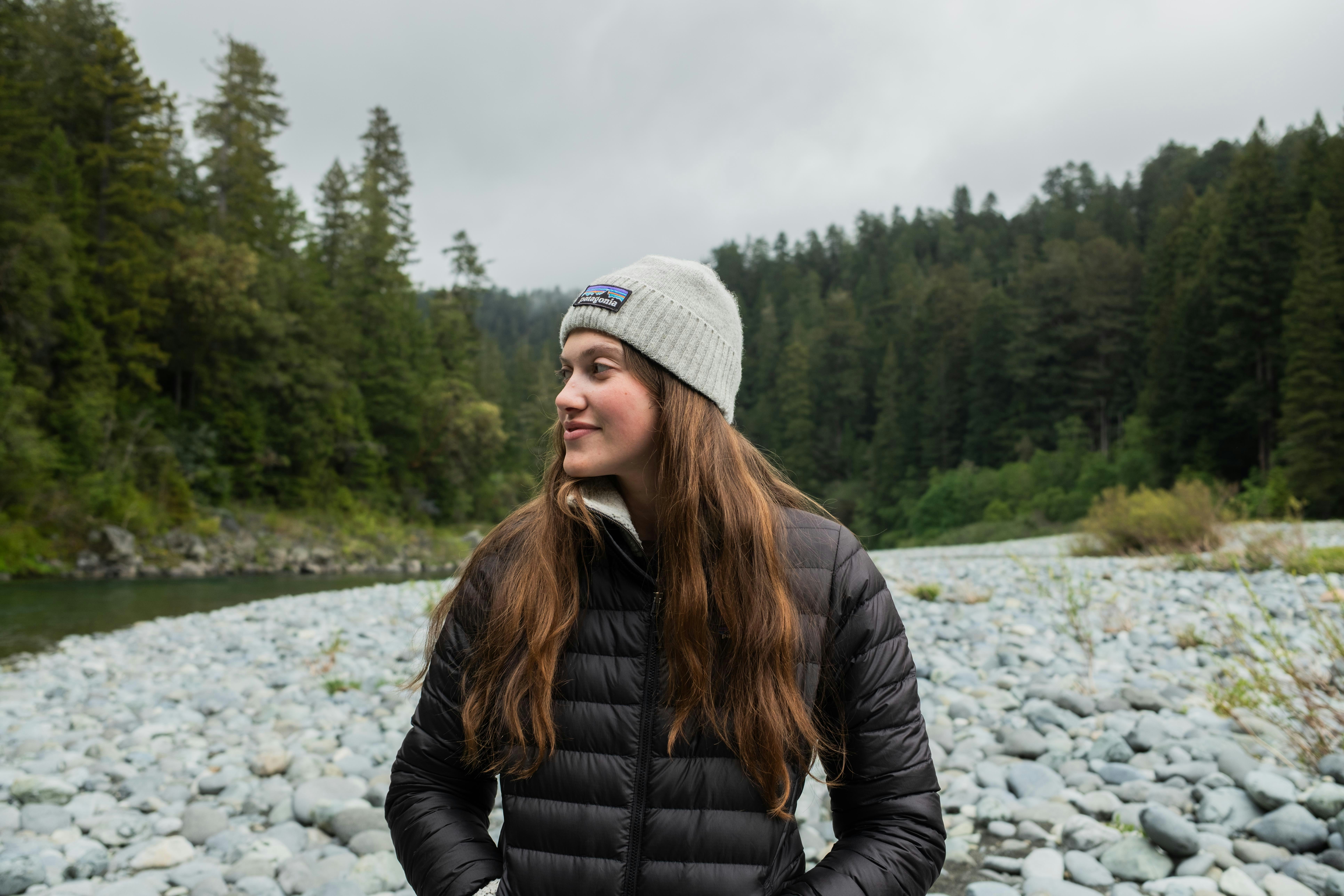 A woman stands beside a rocky river.