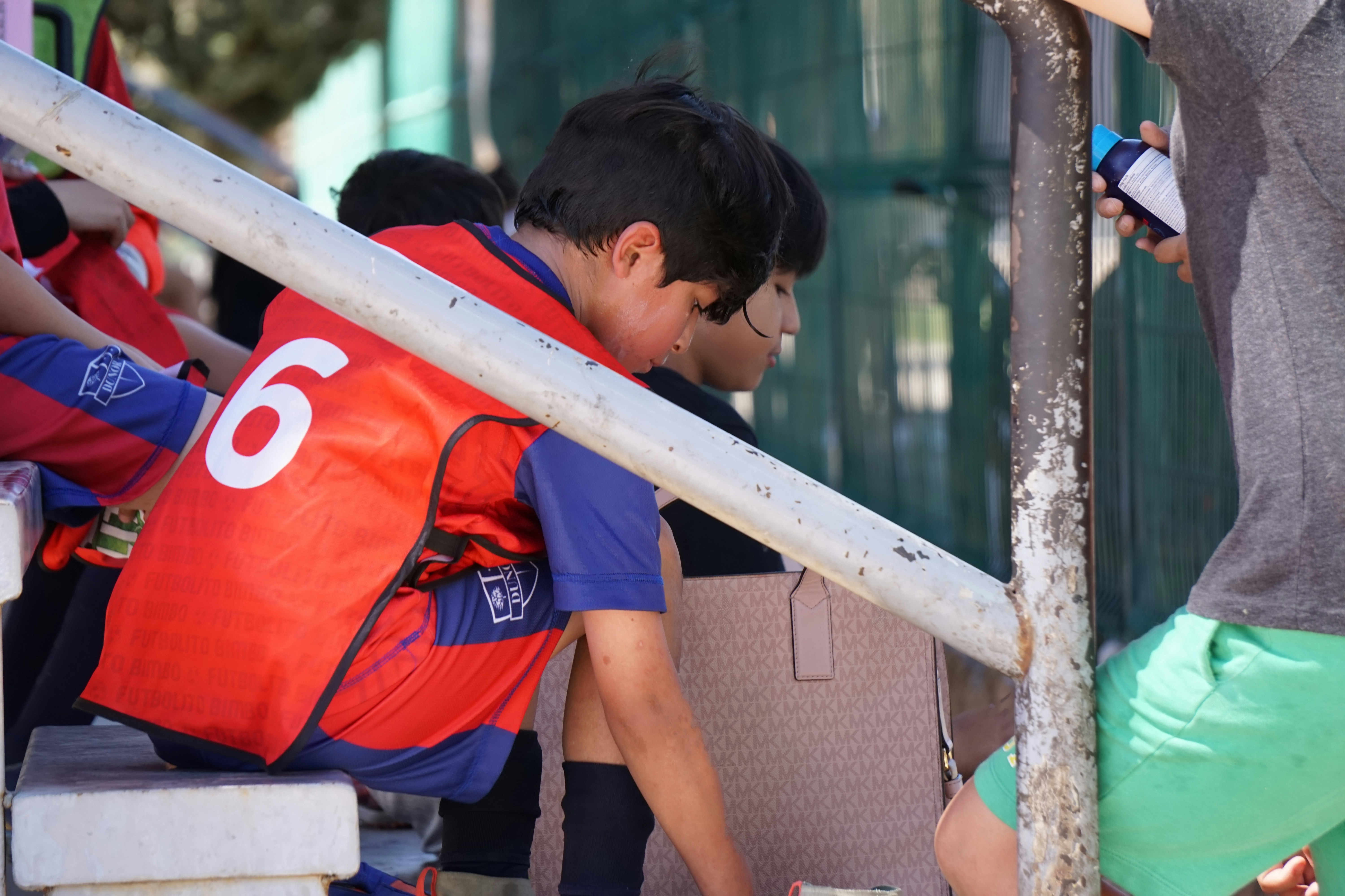 Young soccer players in vibrant jerseys prepare for their match, seated on bleachers with focused expressions.