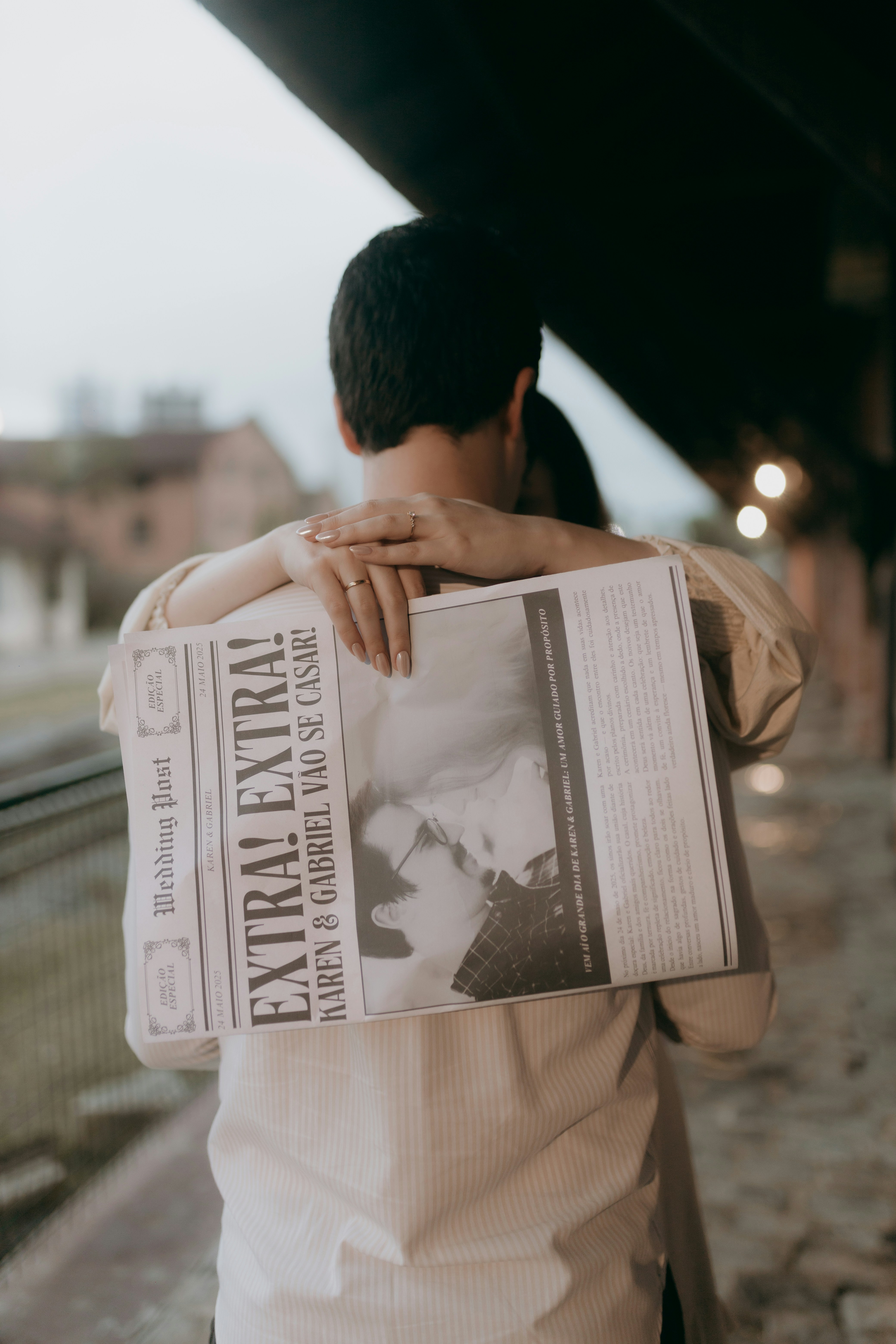 Couple embracing while holding a newspaper announcing their engagement, capturing a moment of joy and connection.