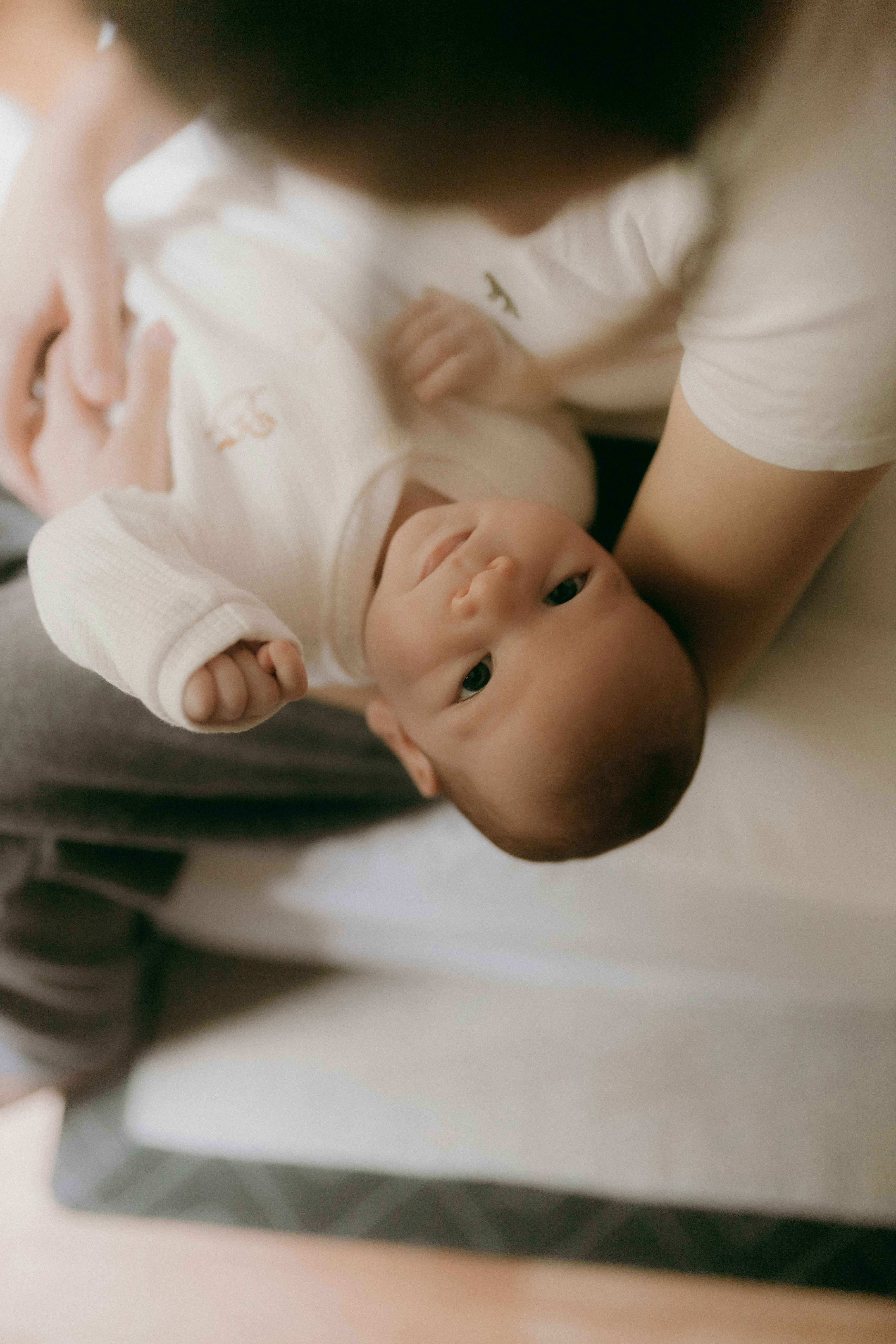 Newborn baby gazing curiously while being held, showcasing a serene and intimate moment between parent and child.