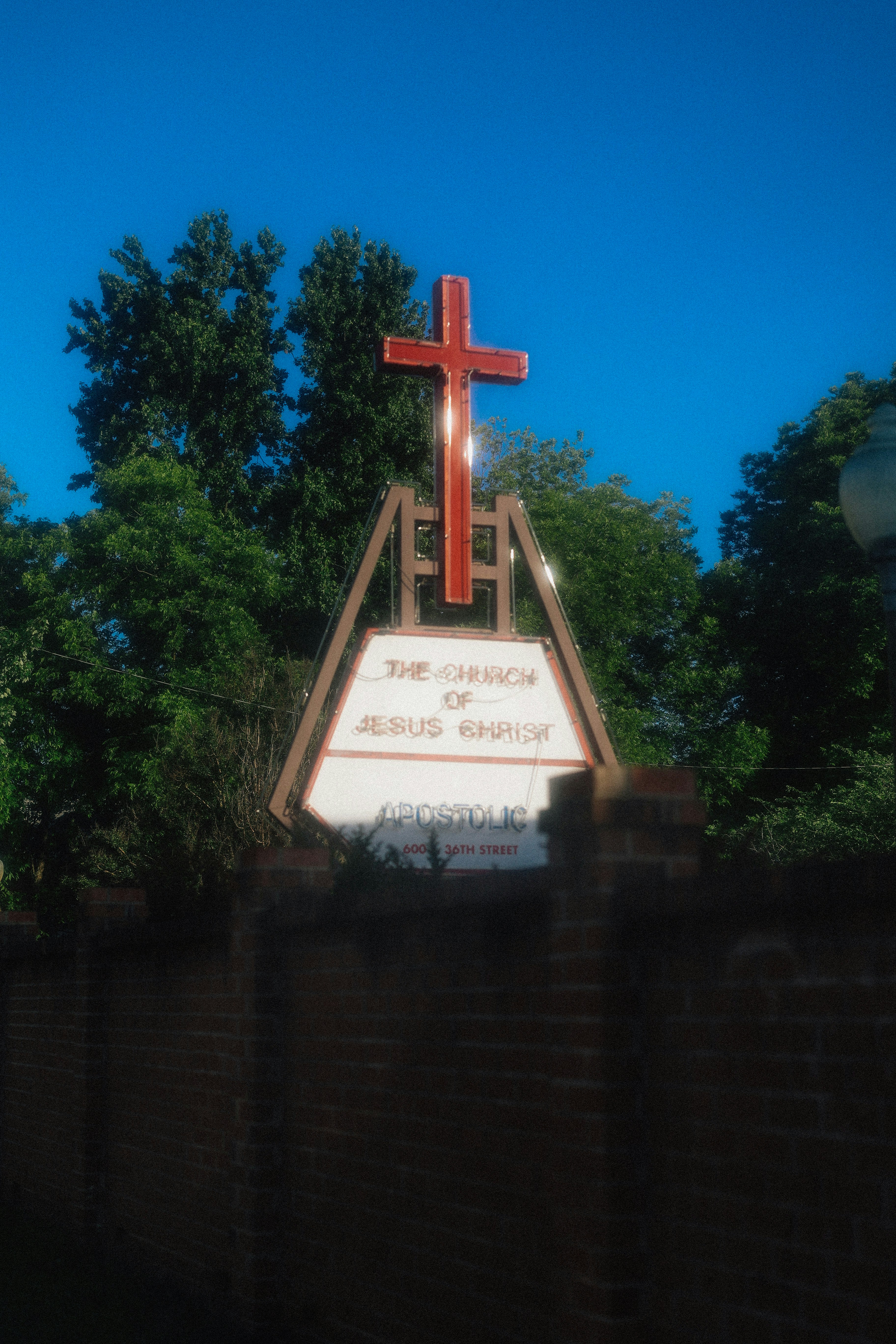 Sign of The Church of Jesus Christ Apostolic framed by lush greenery under a bright blue sky.
