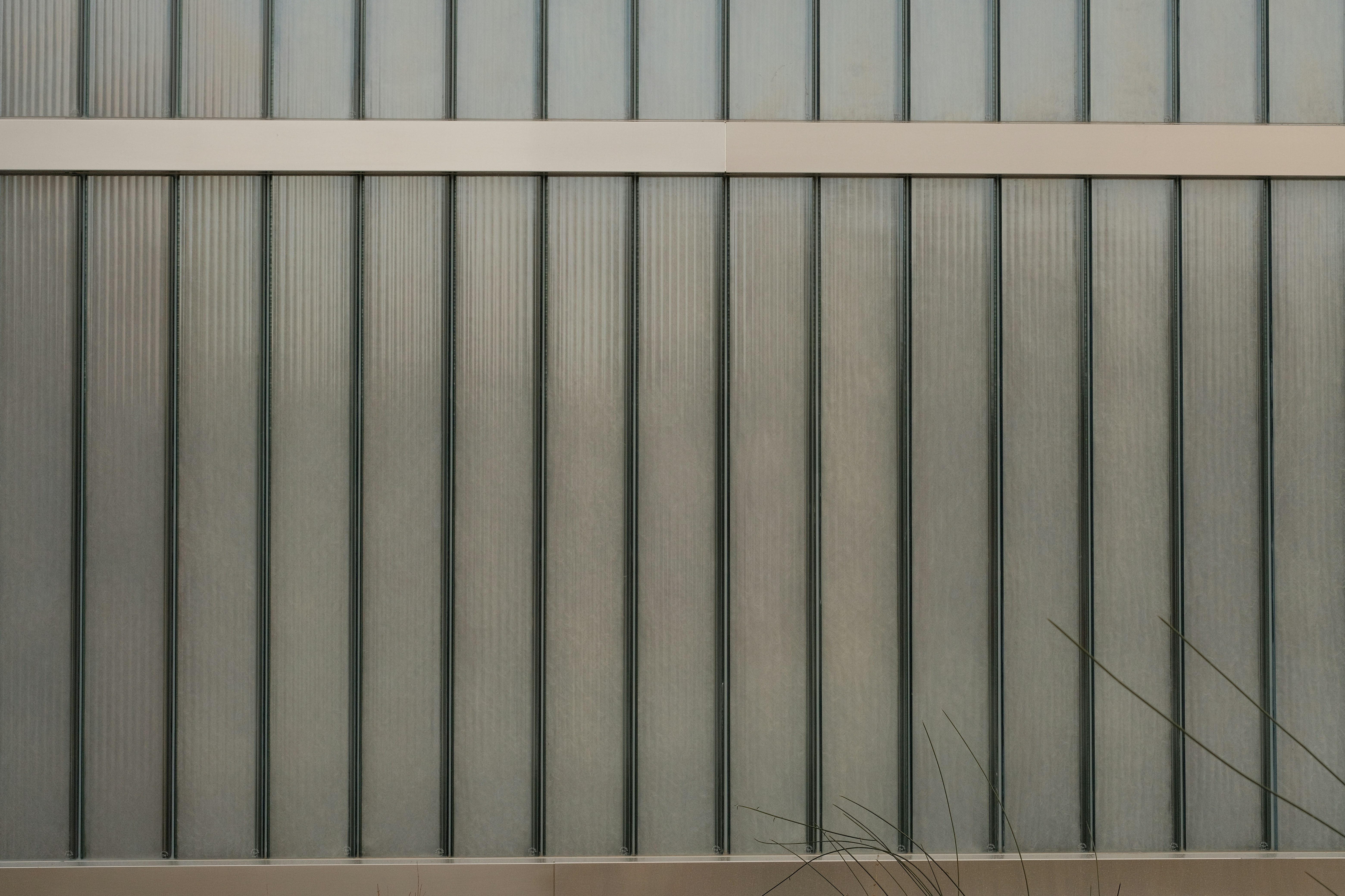 Abstract view of a textured wall featuring vertical lines and muted tones, with subtle natural elements in the foreground.