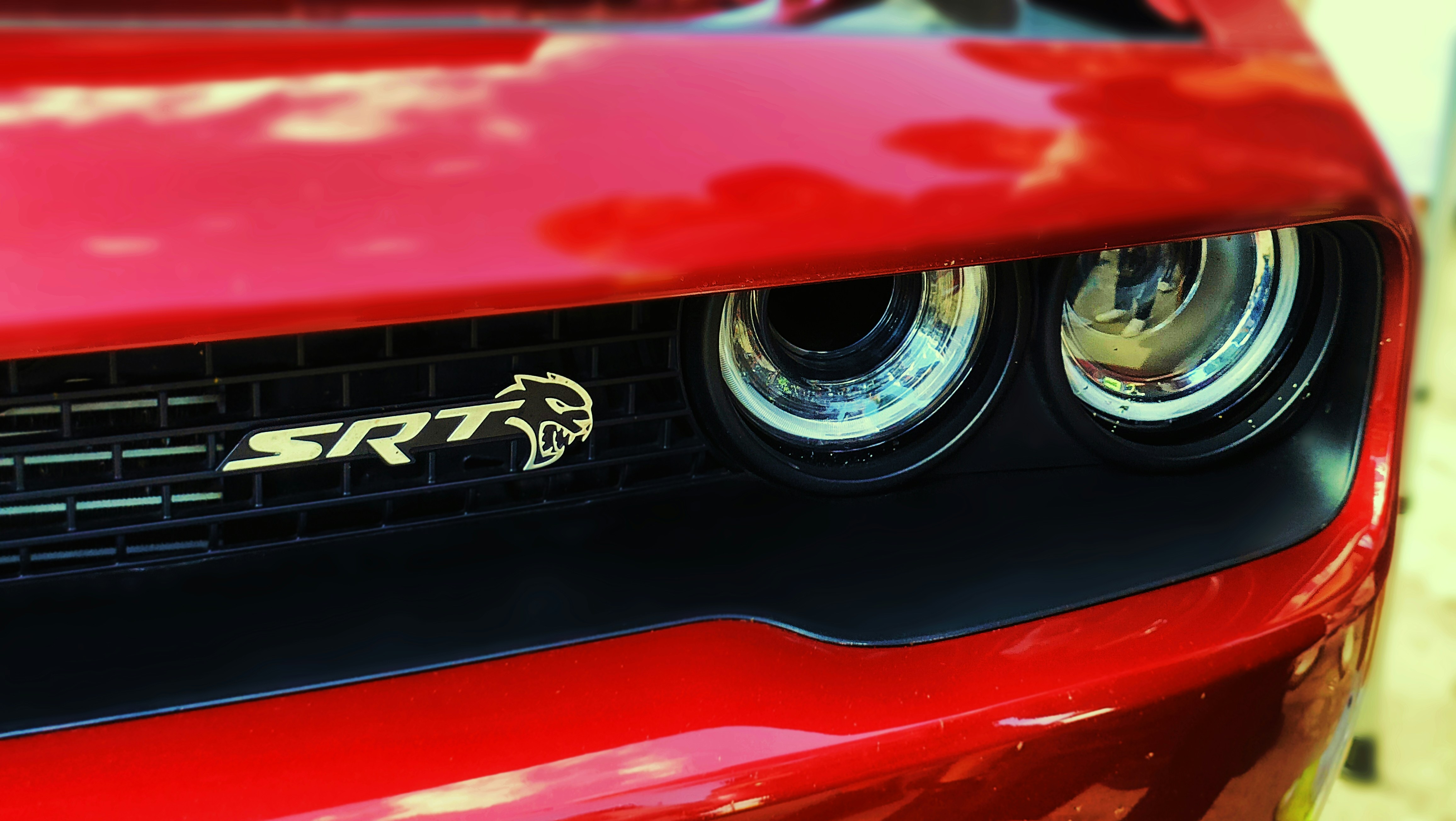 Close-up of a red SRT car's front grille featuring distinctive headlights and emblem. The sleek design emphasizes automotive performance.