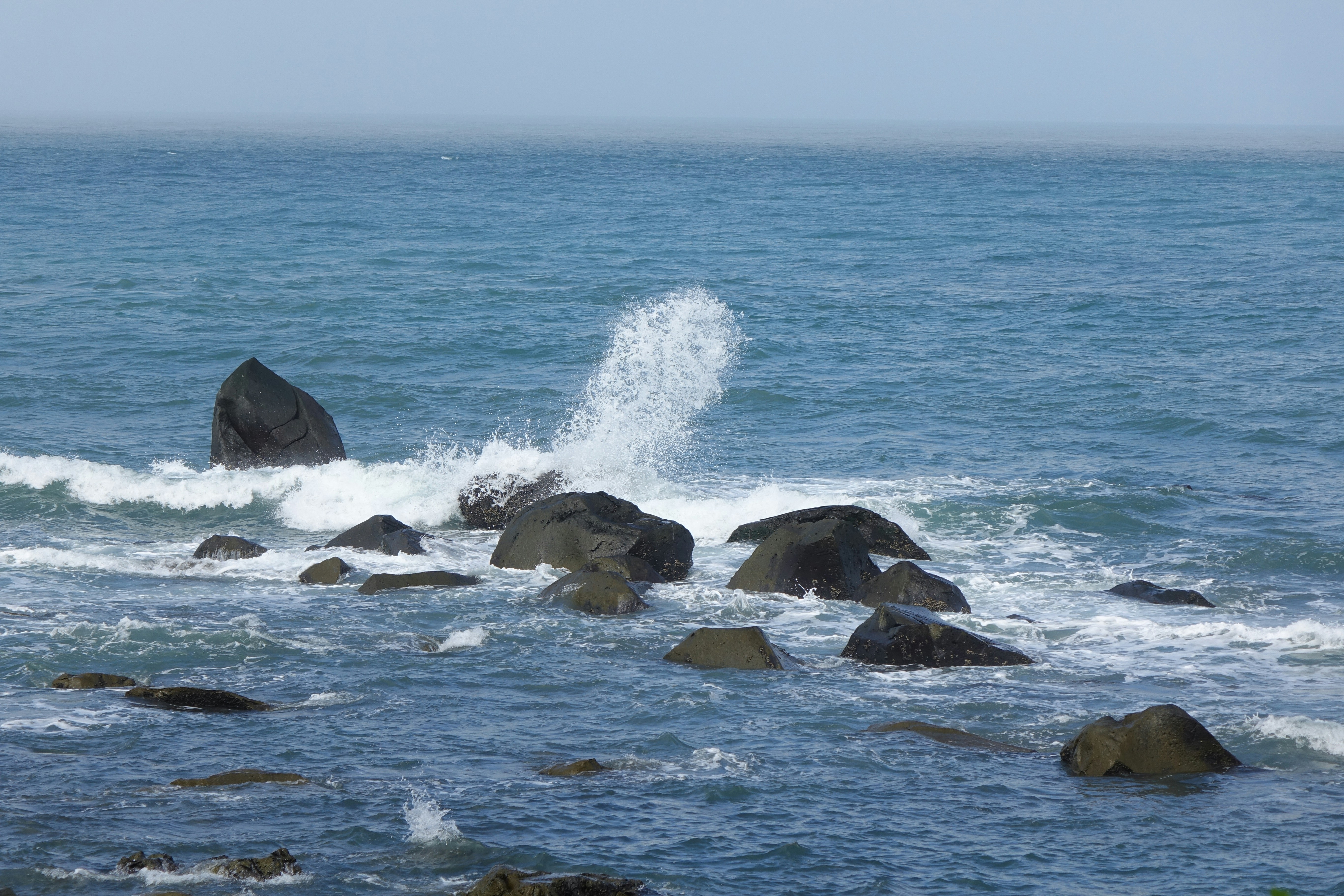 Waves crashing against rugged rocks along a serene coastline, capturing the dynamic interplay between sea and stone.