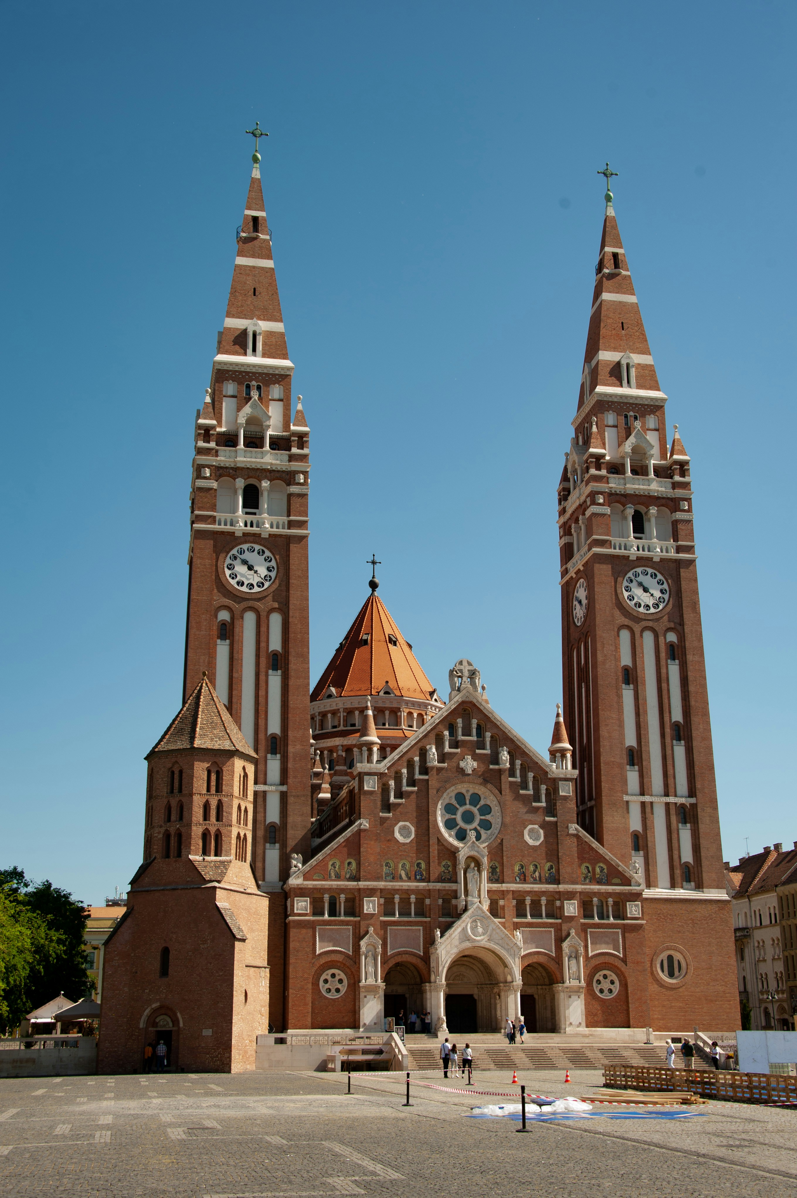 Imposing twin towers frame the grand entrance of a historic church, showcasing intricate brickwork and decorative elements. The clear blue sky enhances the structure's prominence.
