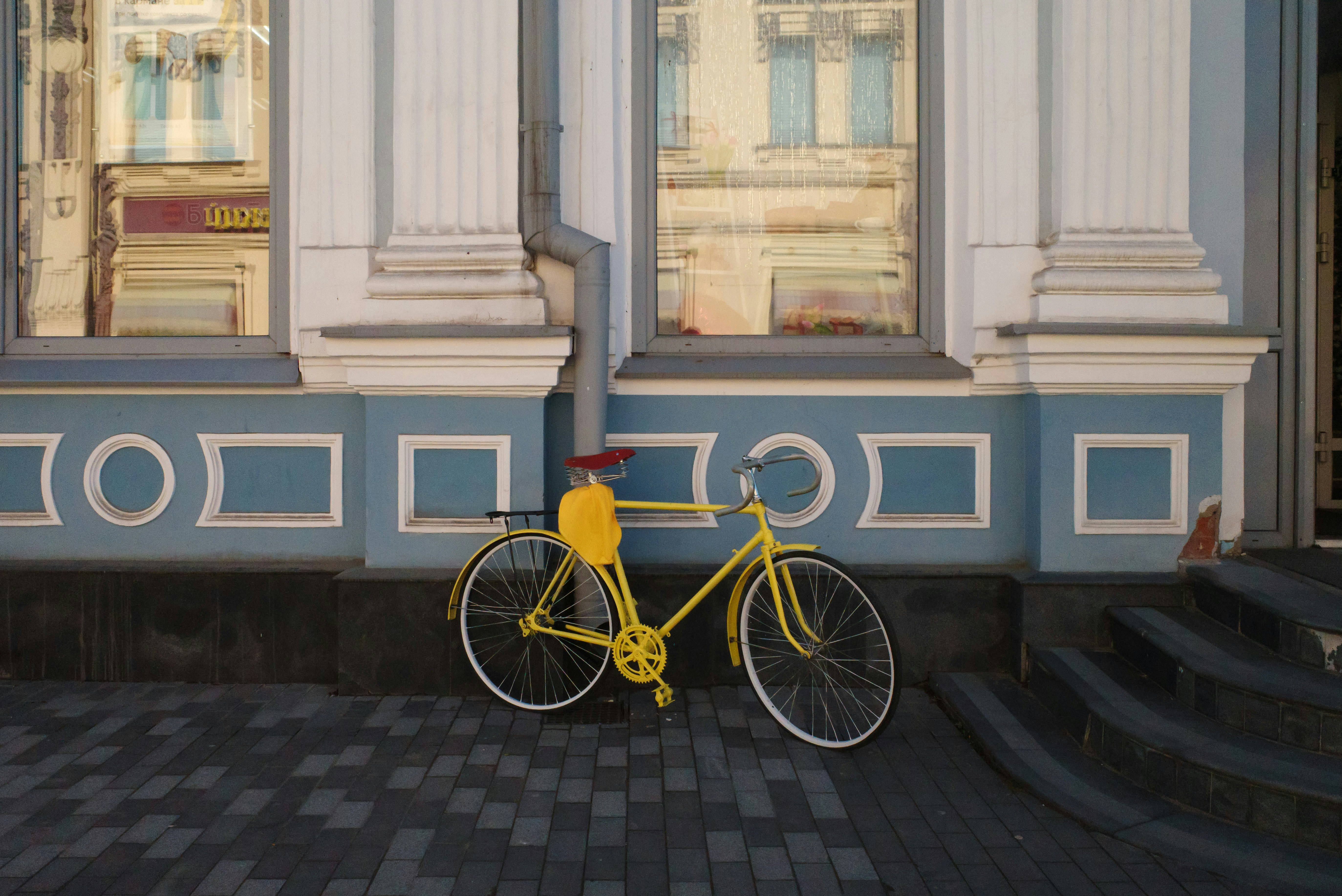 Yellow Bicycle Resting Against a Blue-White Facade on a Quiet Street