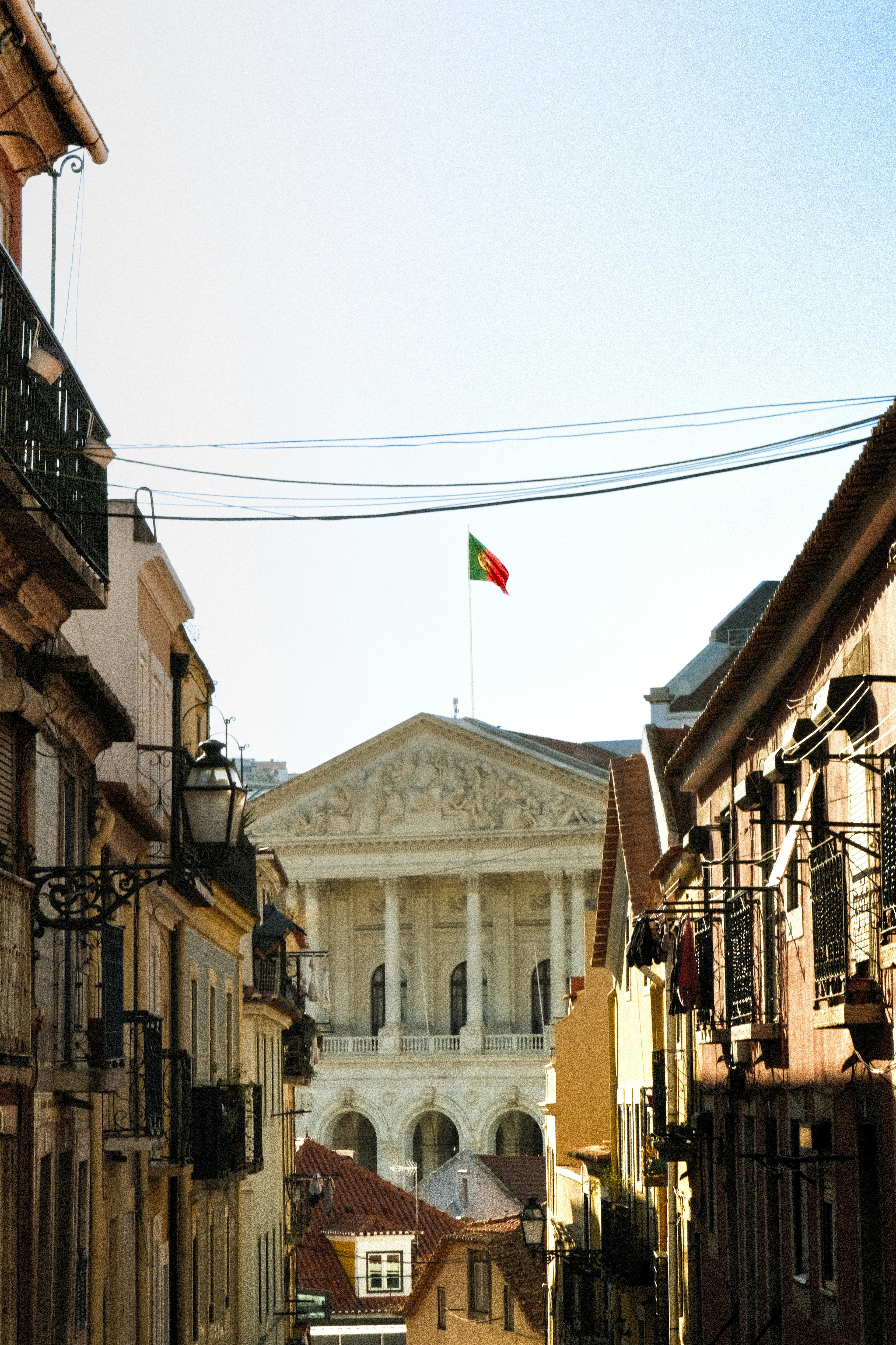 Lisbon Narrow Street Converges on a Neoclassical Facade Under a Flag