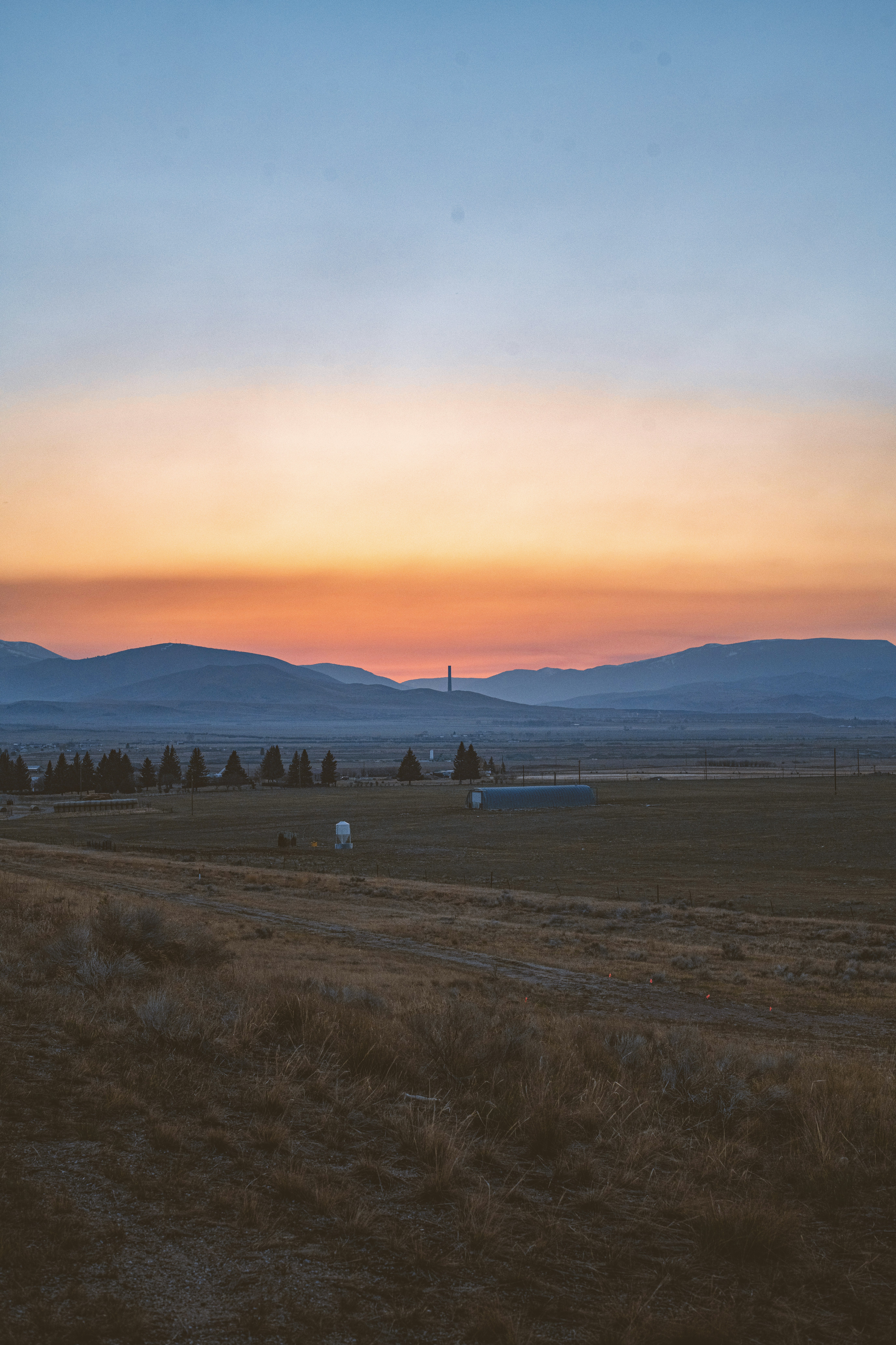 Vast plains under a gradient sky at twilight, with distant mountains silhouetted against the fading light. The scene captures the serene transition from day to night.