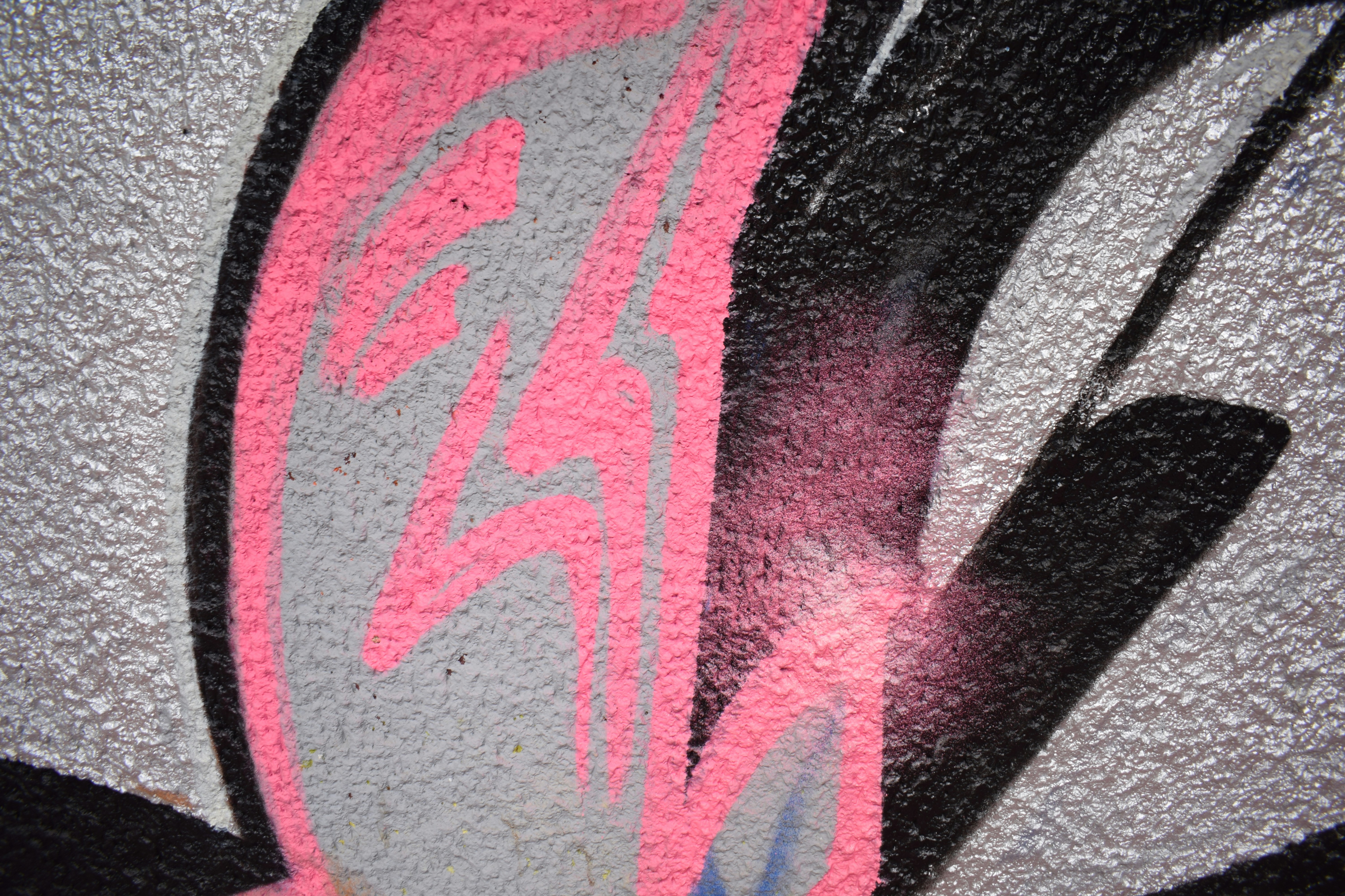 Vibrant graffiti artwork featuring bold pink lines and abstract shapes on a textured wall.