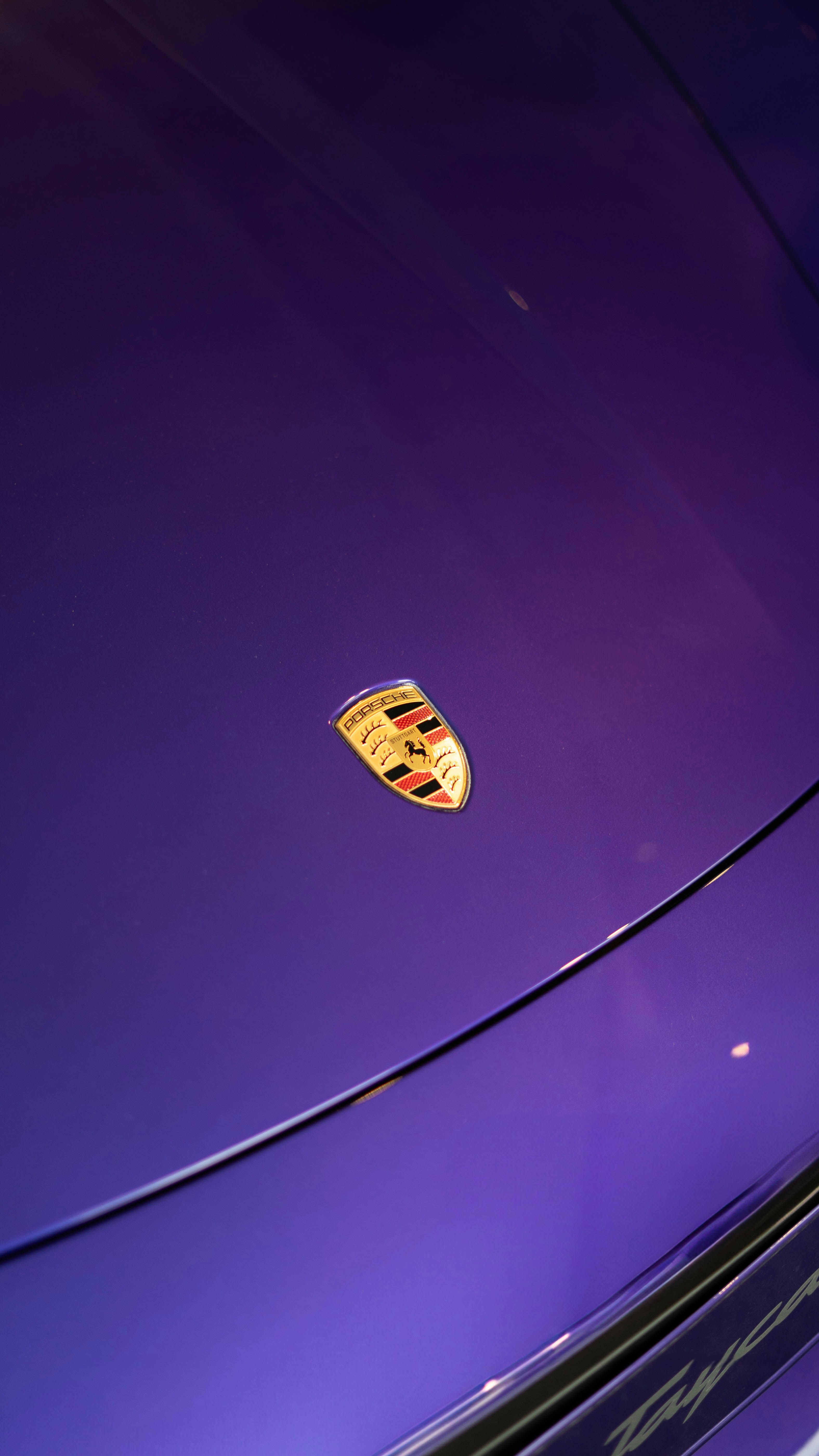 Close-up of a Porsche emblem on a sleek purple car hood, showcasing luxury automotive design.