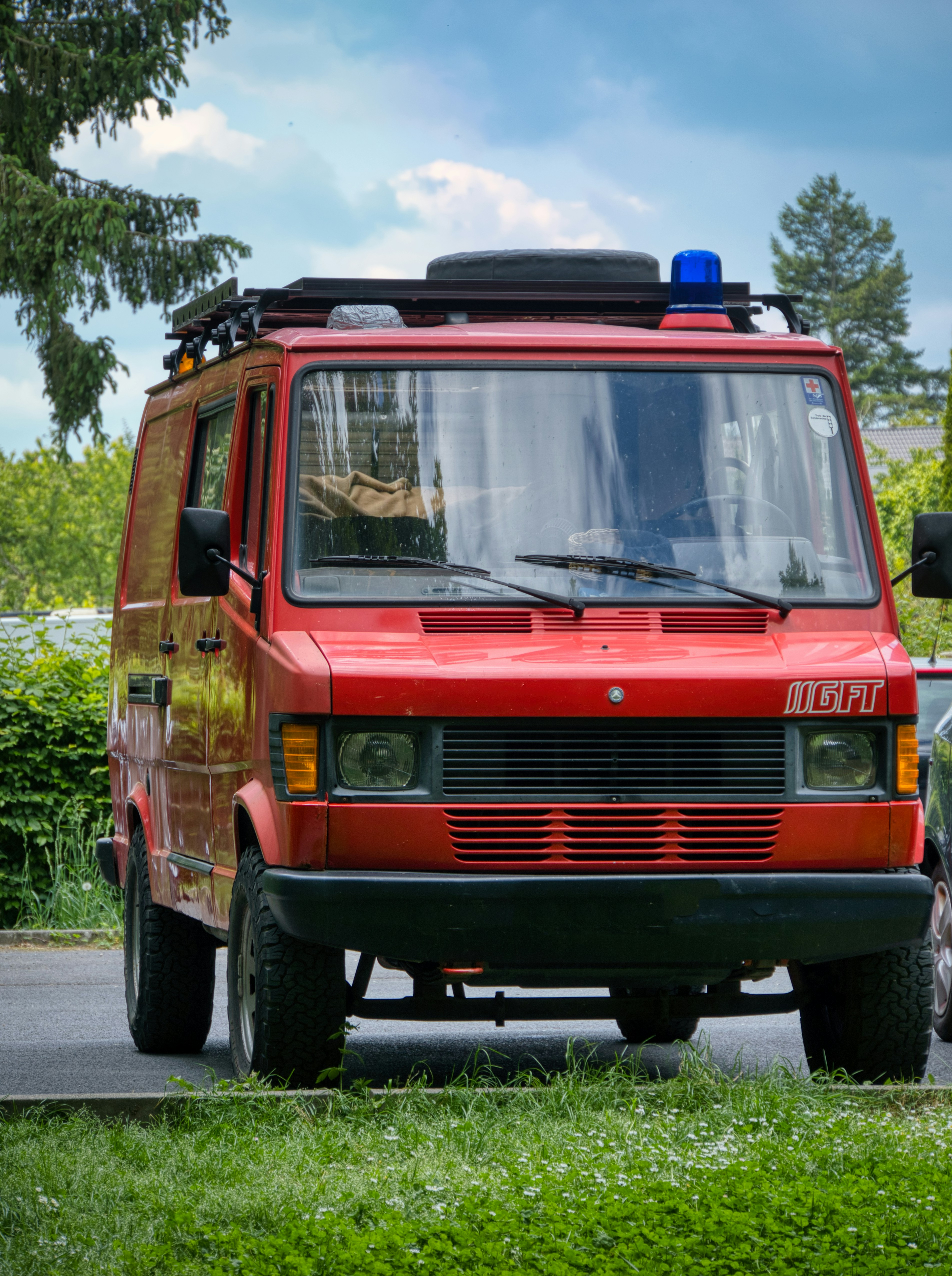 Front-Facing Red Utility Van with Rooftop Gear and Blue Beacon