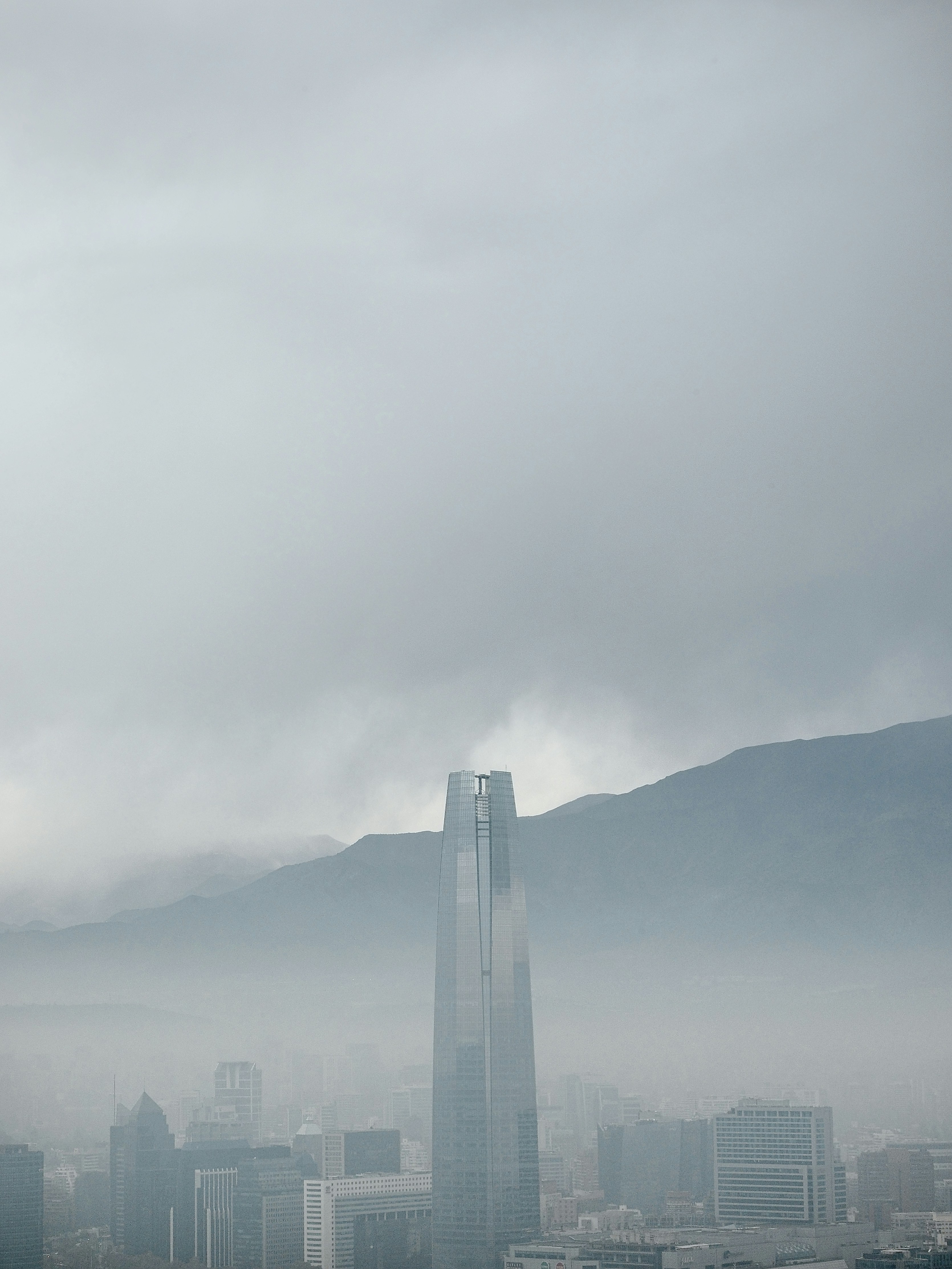 A towering skyscraper emerges from a blanket of fog, surrounded by a muted cityscape and distant mountains. The scene conveys a sense of mystery and tranquility.