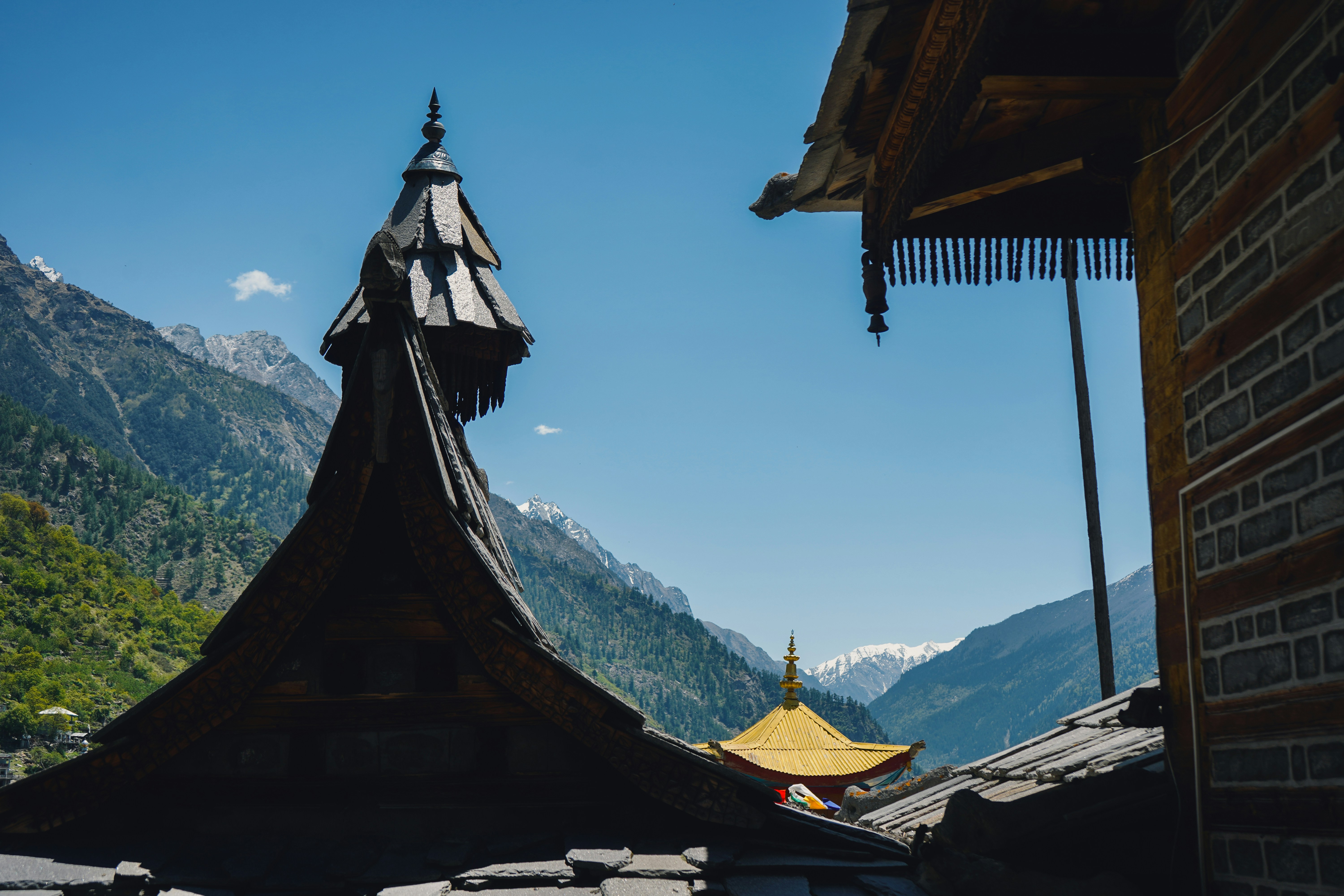Intricate rooftops of traditional architecture framed by towering mountains under a clear blue sky.
