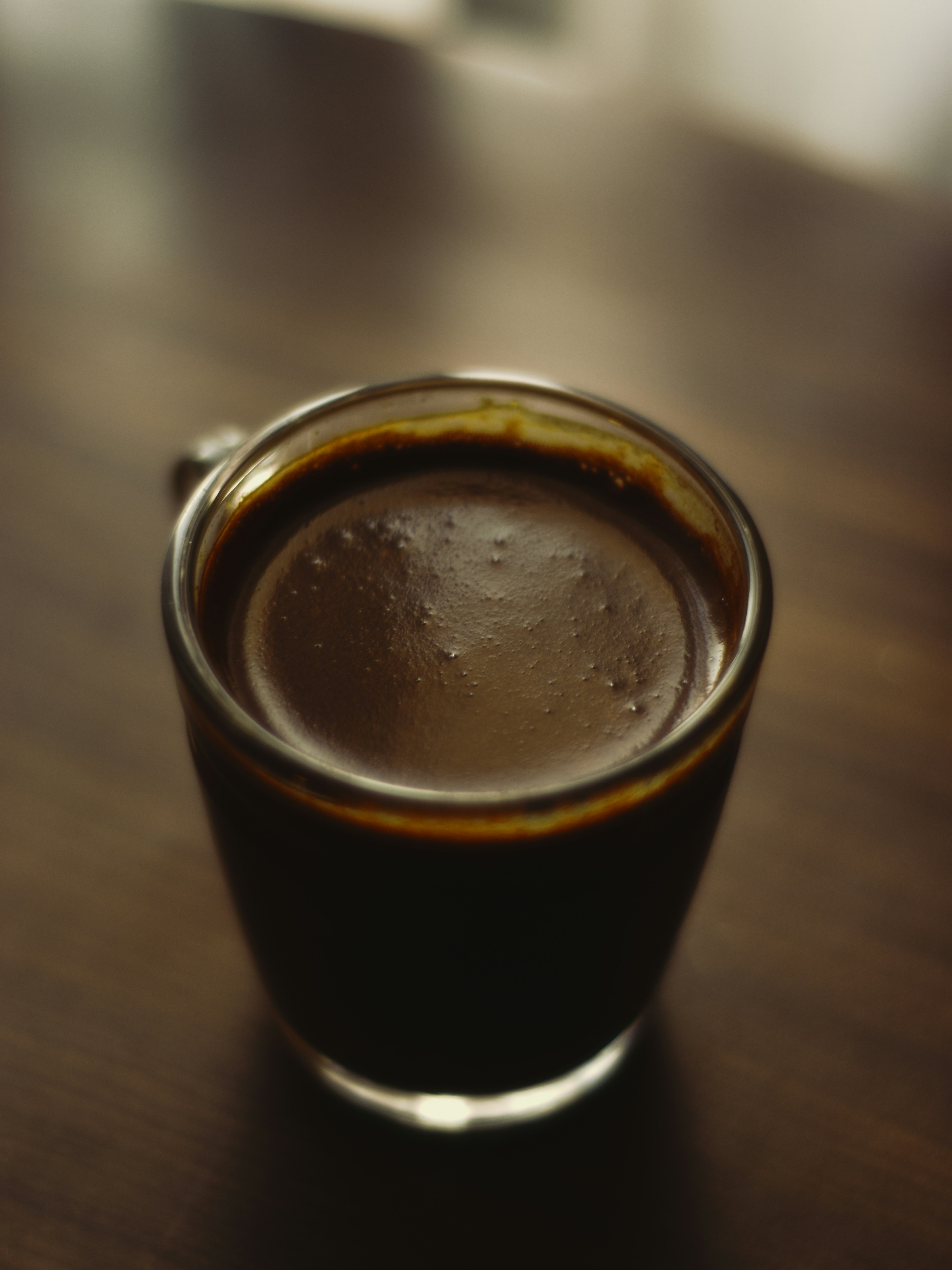 Rich espresso in a clear glass cup resting on a wooden table, highlighting its velvety texture and deep color.
