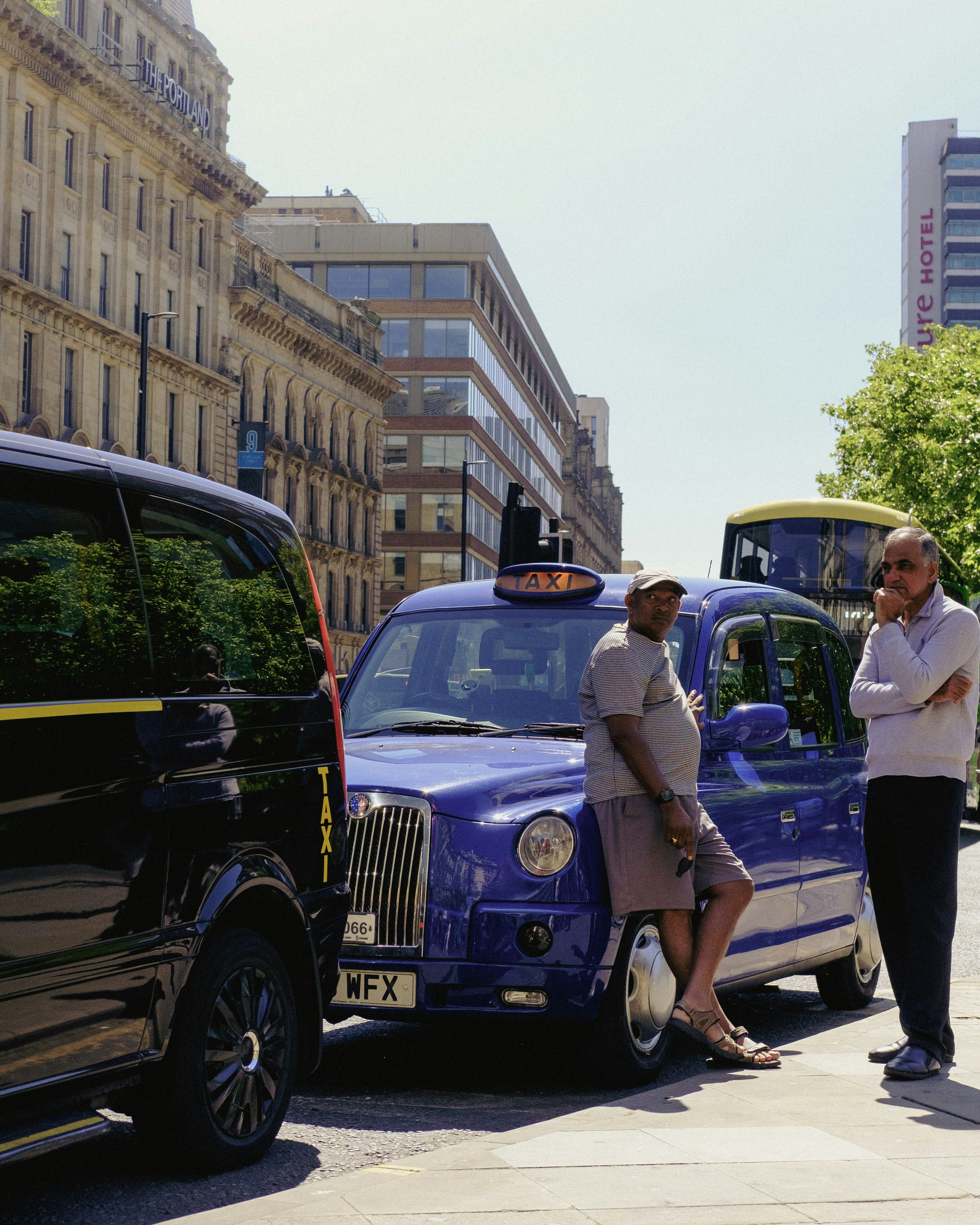 Taxi Drivers | Men near a blue taxi on a city street.