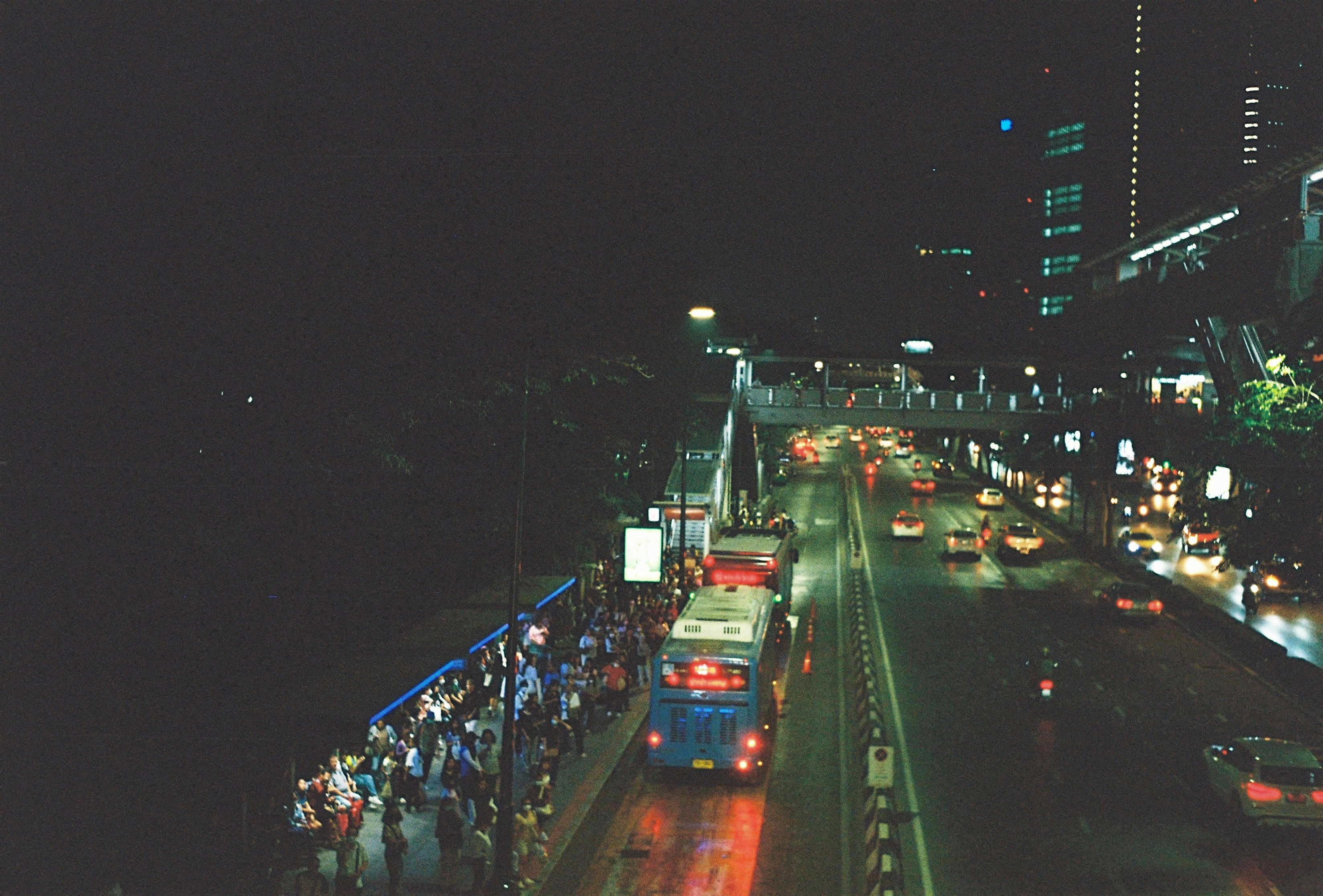 Bustling city street at night, showcasing a busy bus stop and flowing traffic illuminated by streetlights and vehicle headlights.