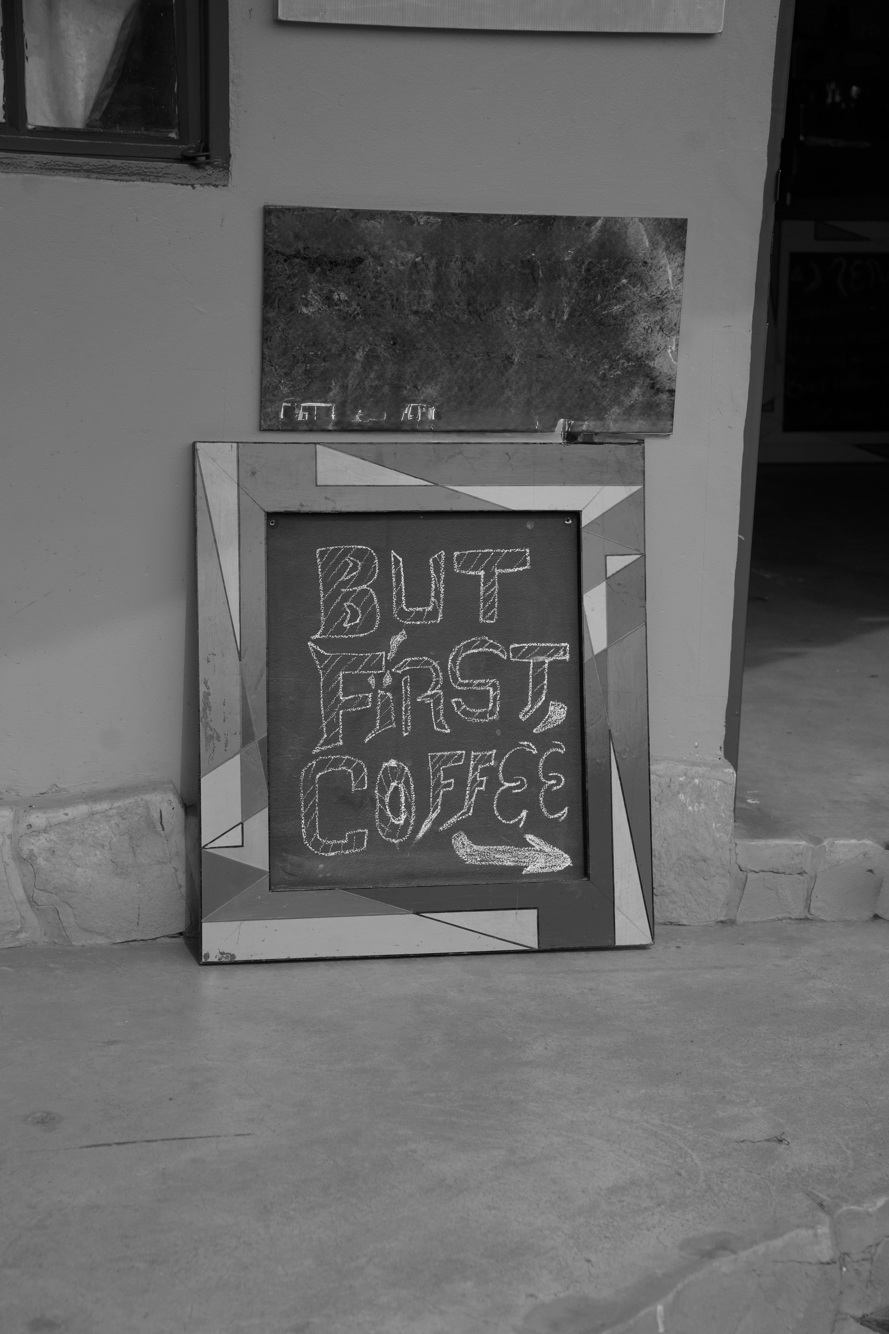Chalkboard sign with the phrase 'BUT FIRST, COFFEE' framed in a colorful border, inviting patrons to enjoy a cup of coffee.