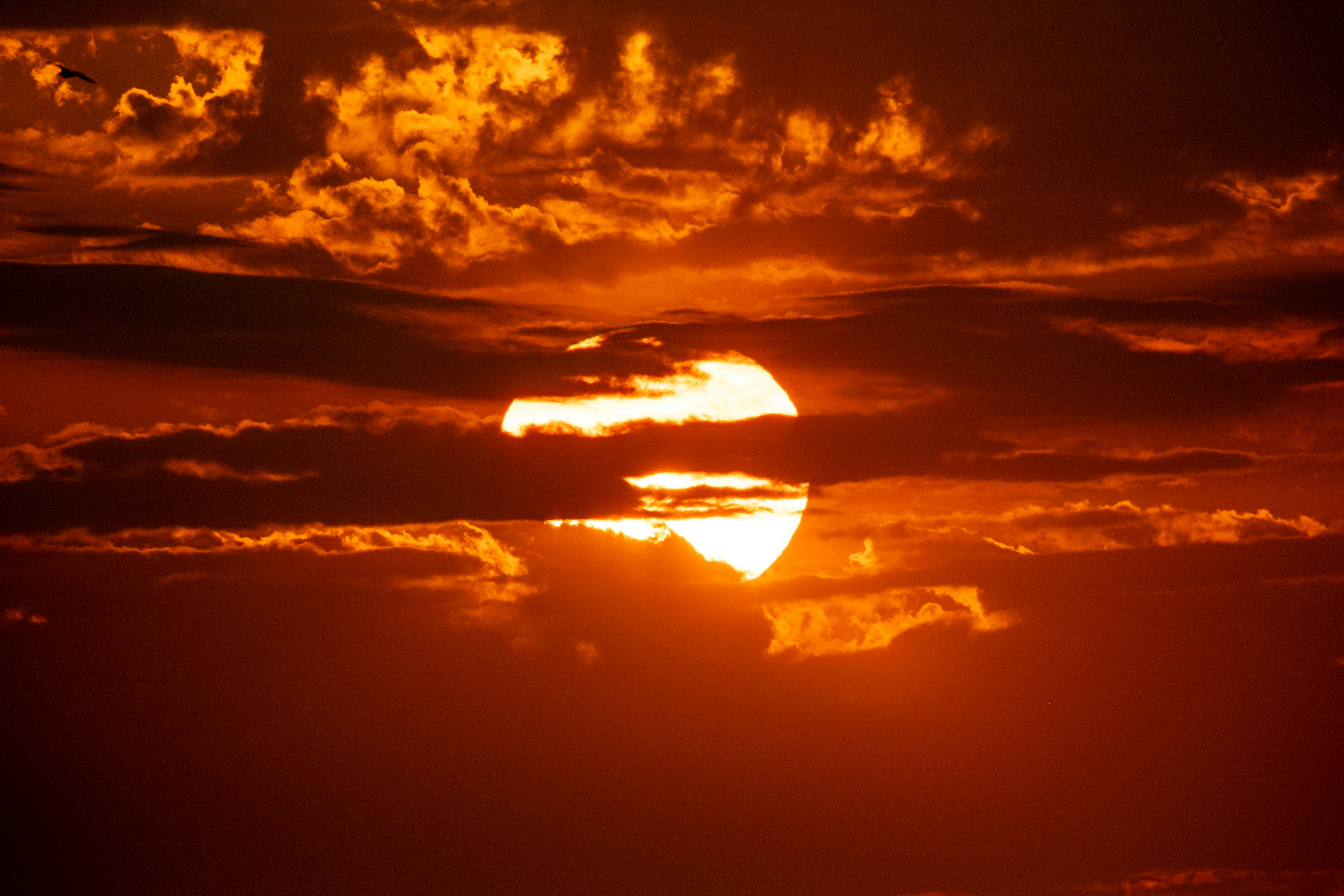 Vibrant sunset with the sun partially obscured by clouds, casting an orange glow across the sky.