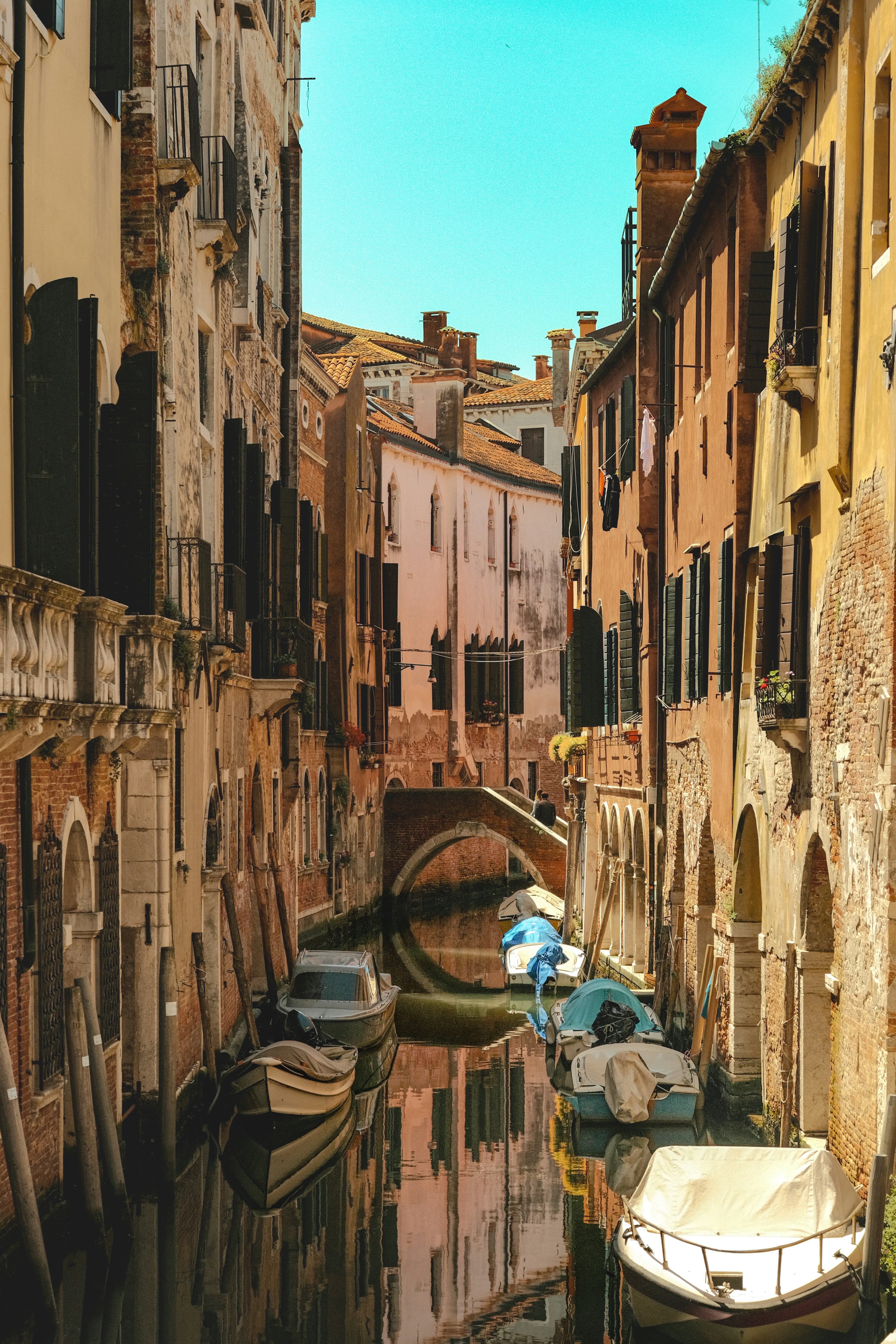 Sunlit Venetian Canal: Timeworn Walls, Moored Boats, and a Quiet Arch Bridge