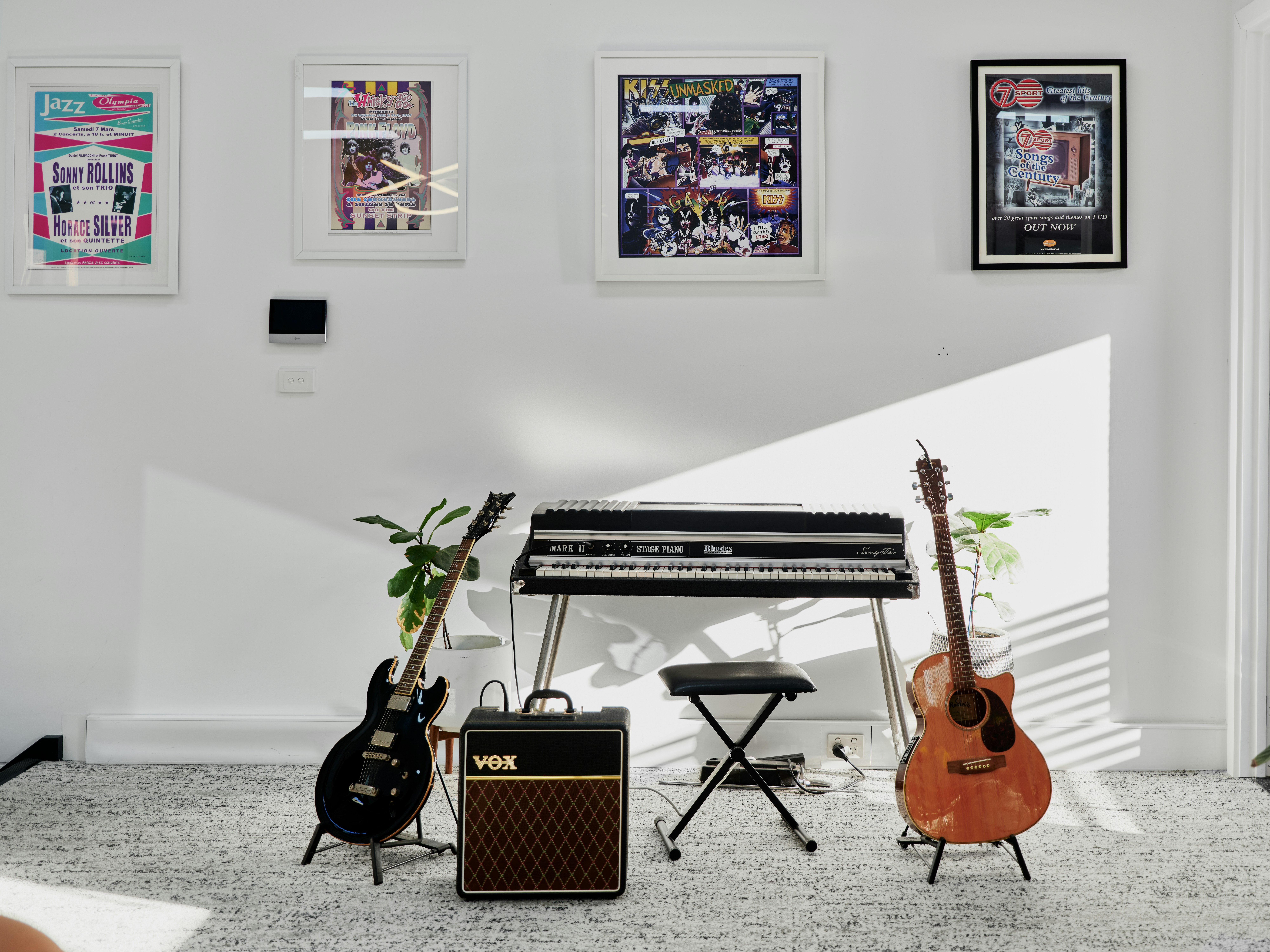 A vibrant music setup featuring an electric guitar, acoustic guitar, keyboard, and amplifier, surrounded by framed art on the wall. Natural light streams in, enhancing the artistic ambiance.
