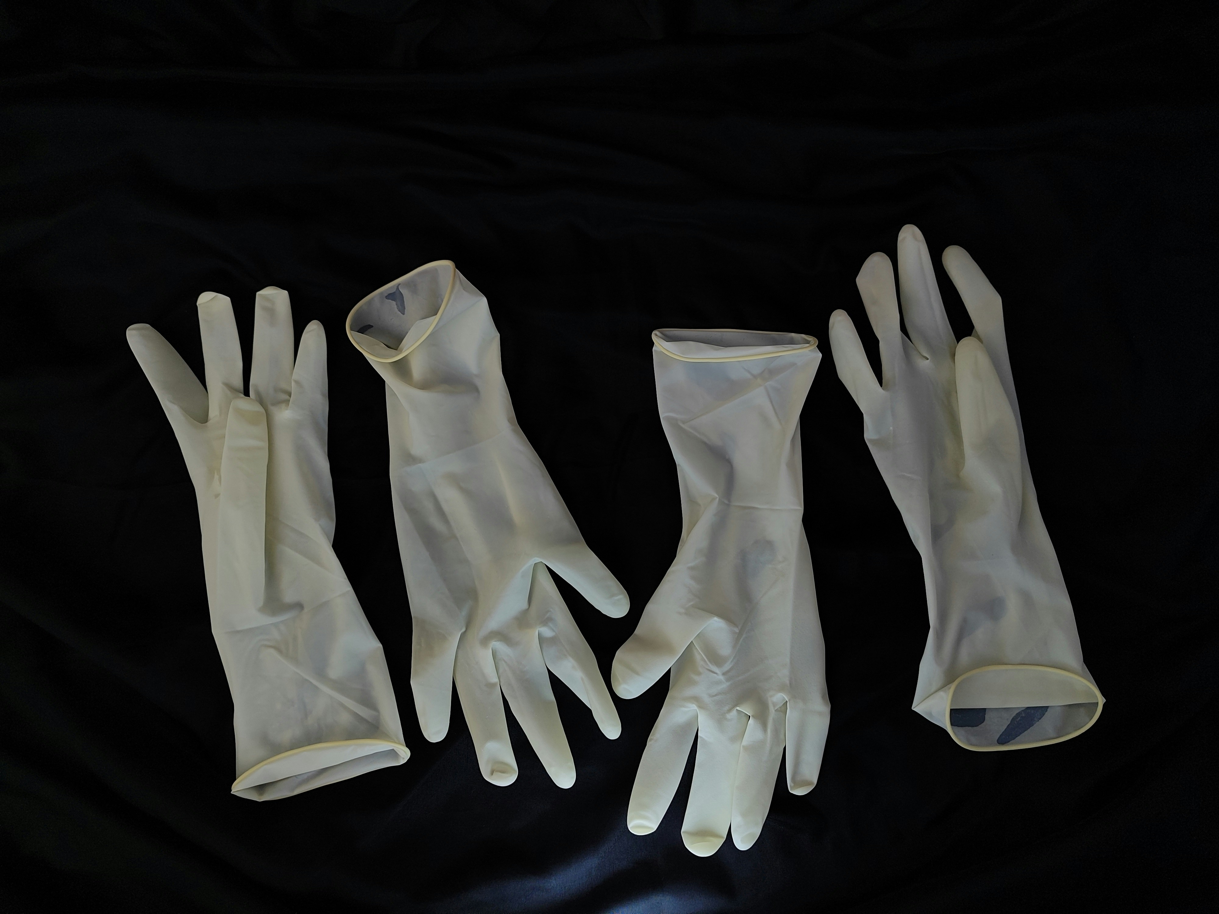Four surgical gloves are displayed on a dark surface.
