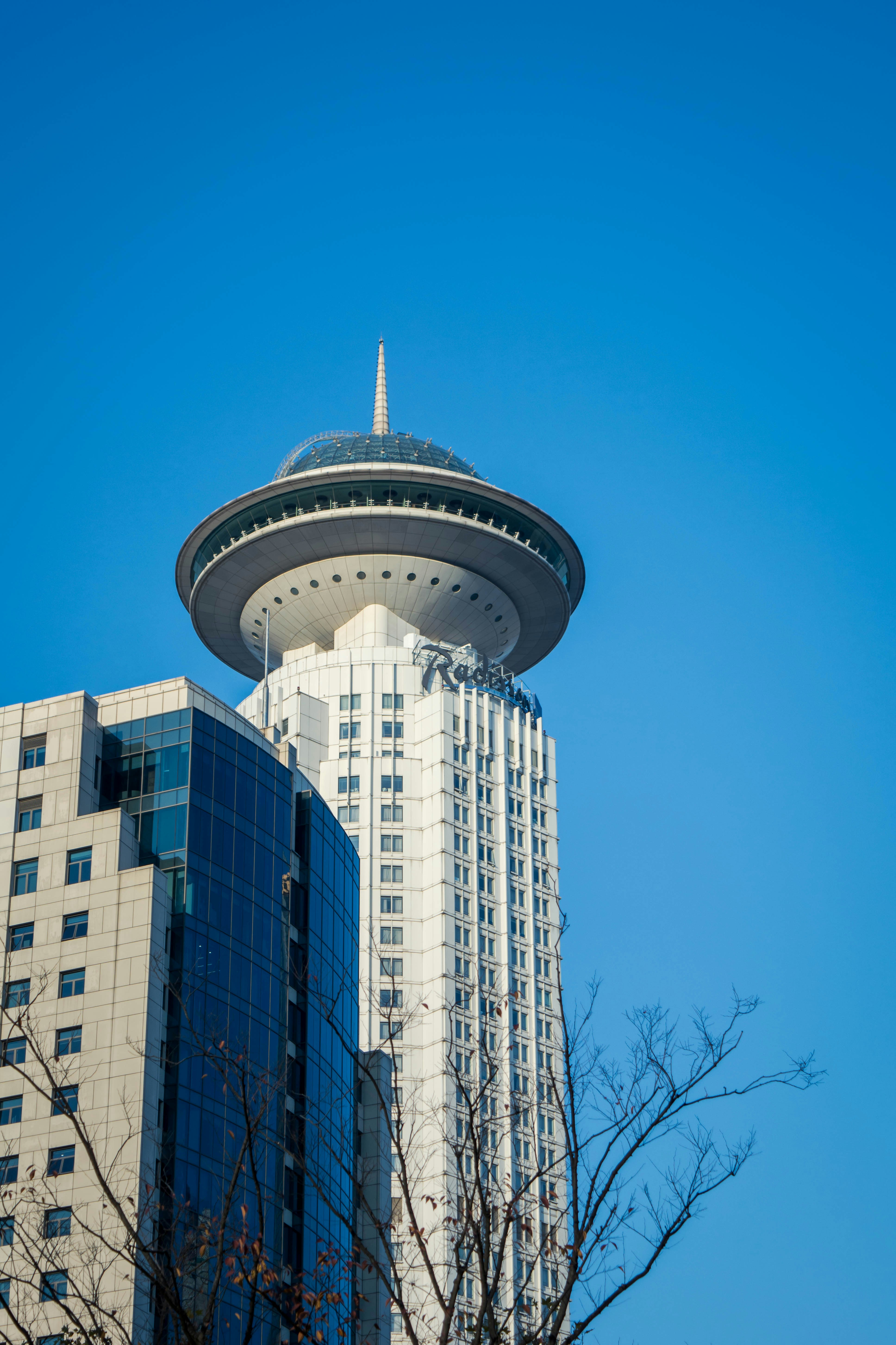 A striking skyscraper with a unique observation deck towers against a clear blue sky, showcasing modern architectural design.
