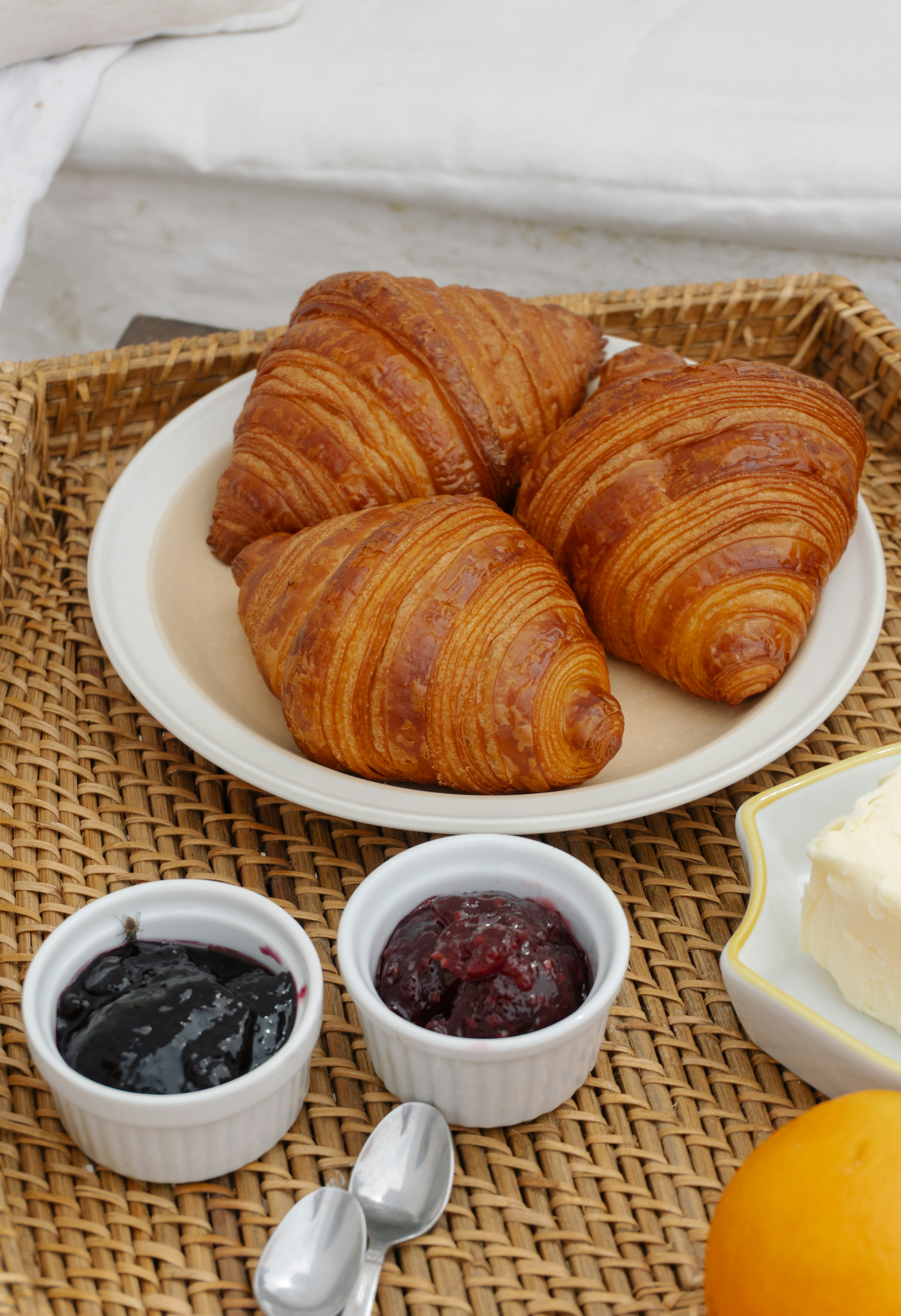 Fresh croissants and jams on a woven tray.