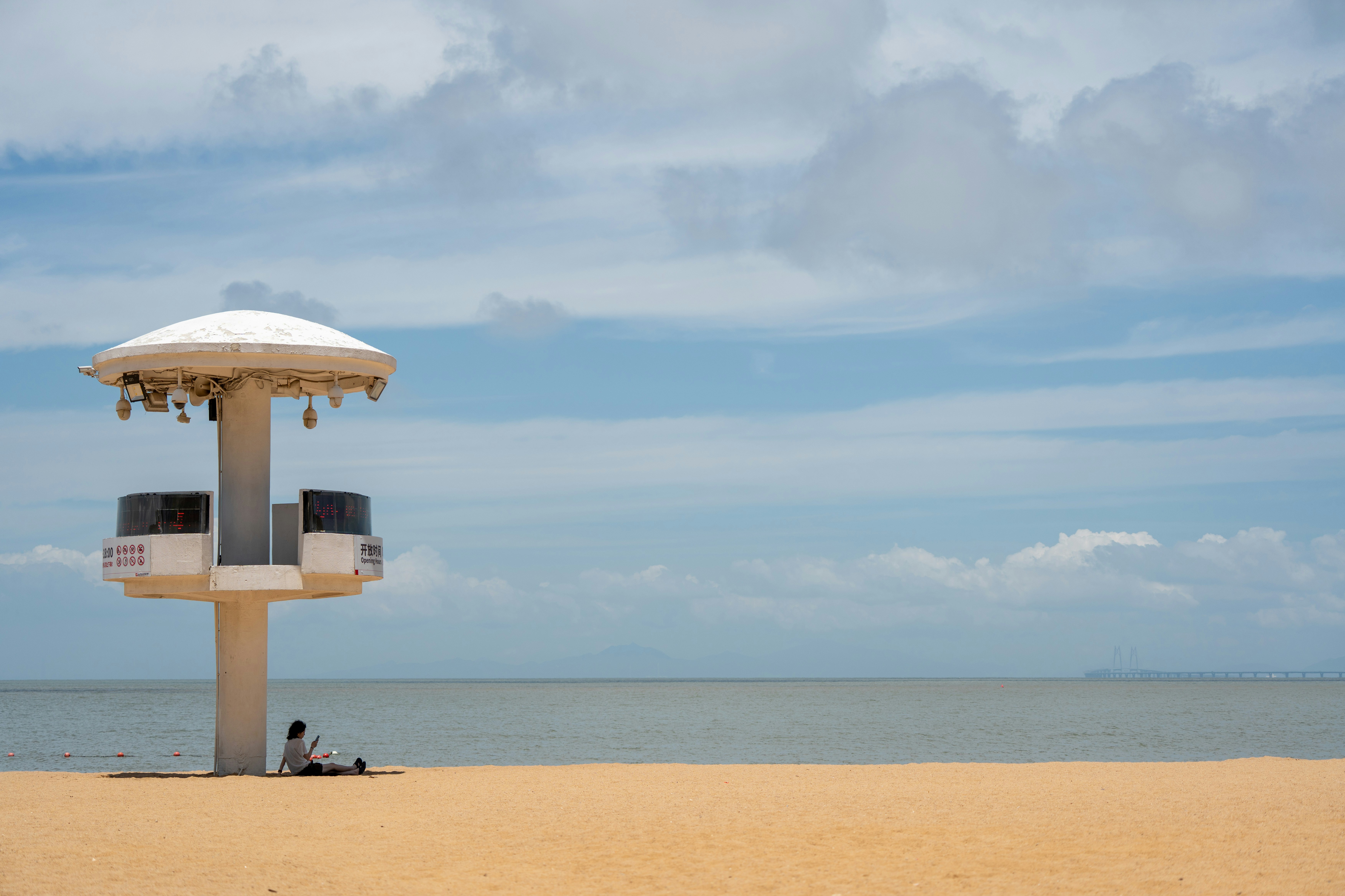A beach with beacon | A person sits on the beach under the sky.