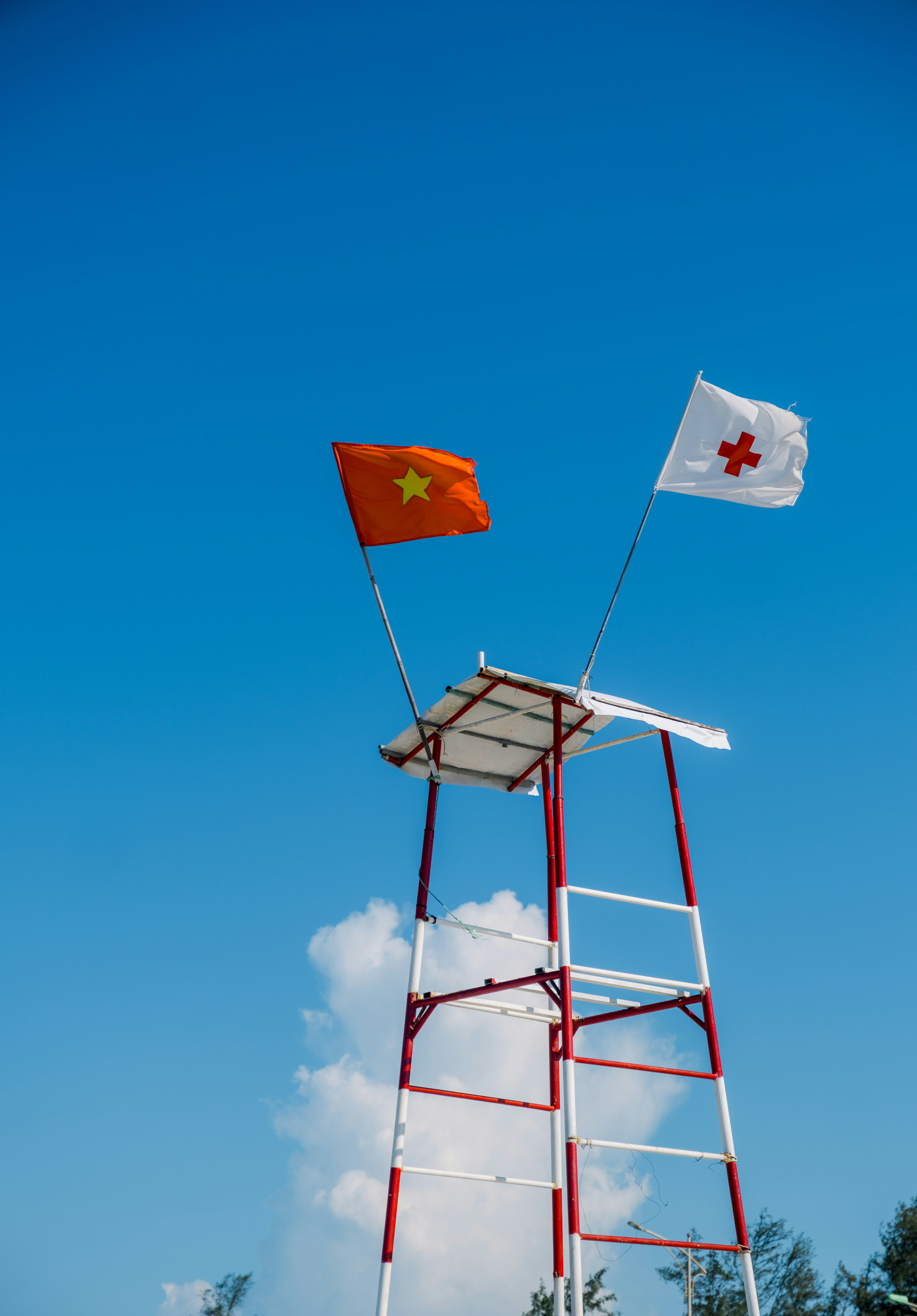 Flags at the Summit: Red Cross and Sun-Ward Flags atop a Tower Against a Clear Blue Sky