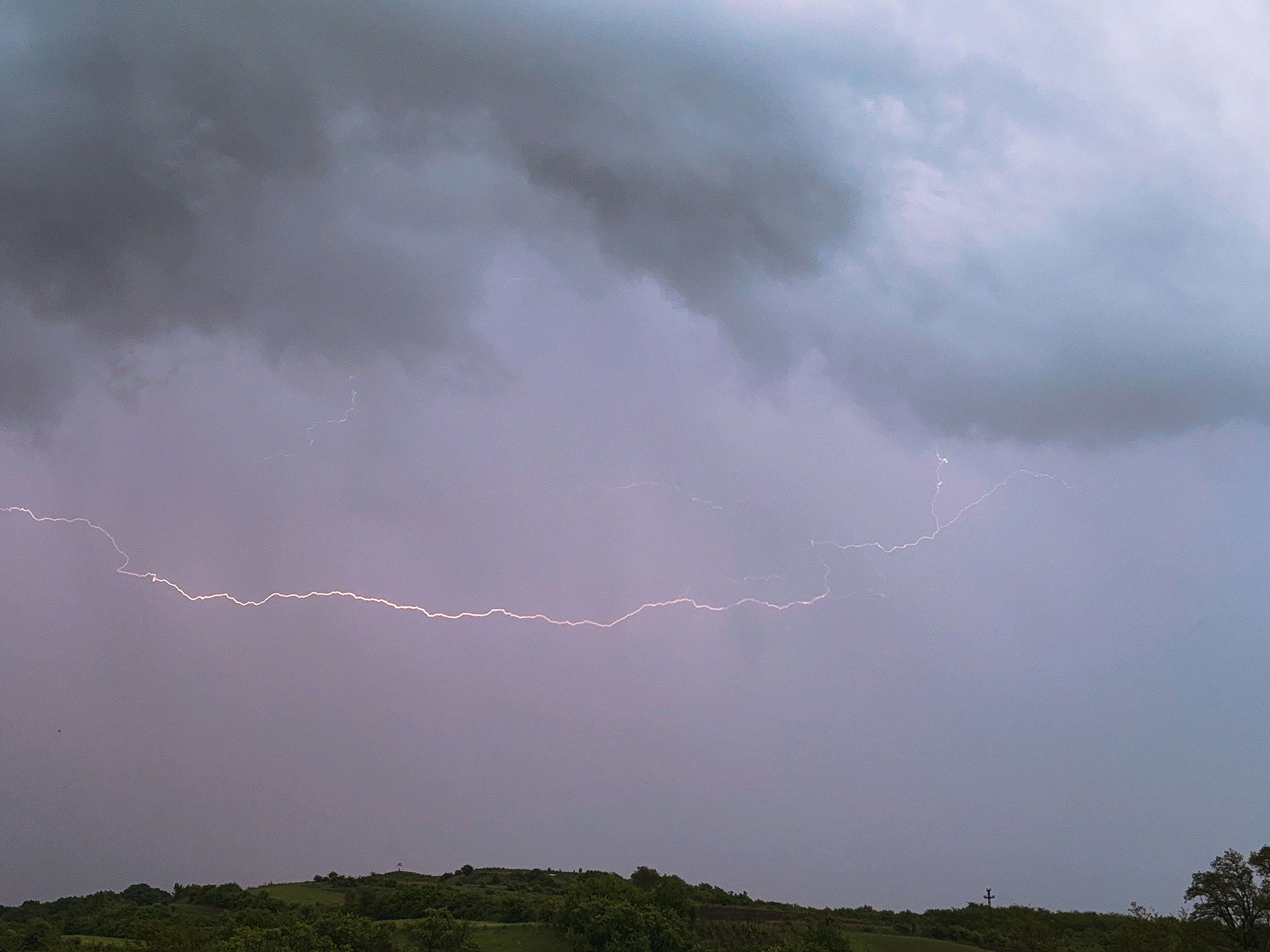A dramatic lightning strike illuminates the stormy sky above rolling green hills, capturing the raw power of nature's fury.