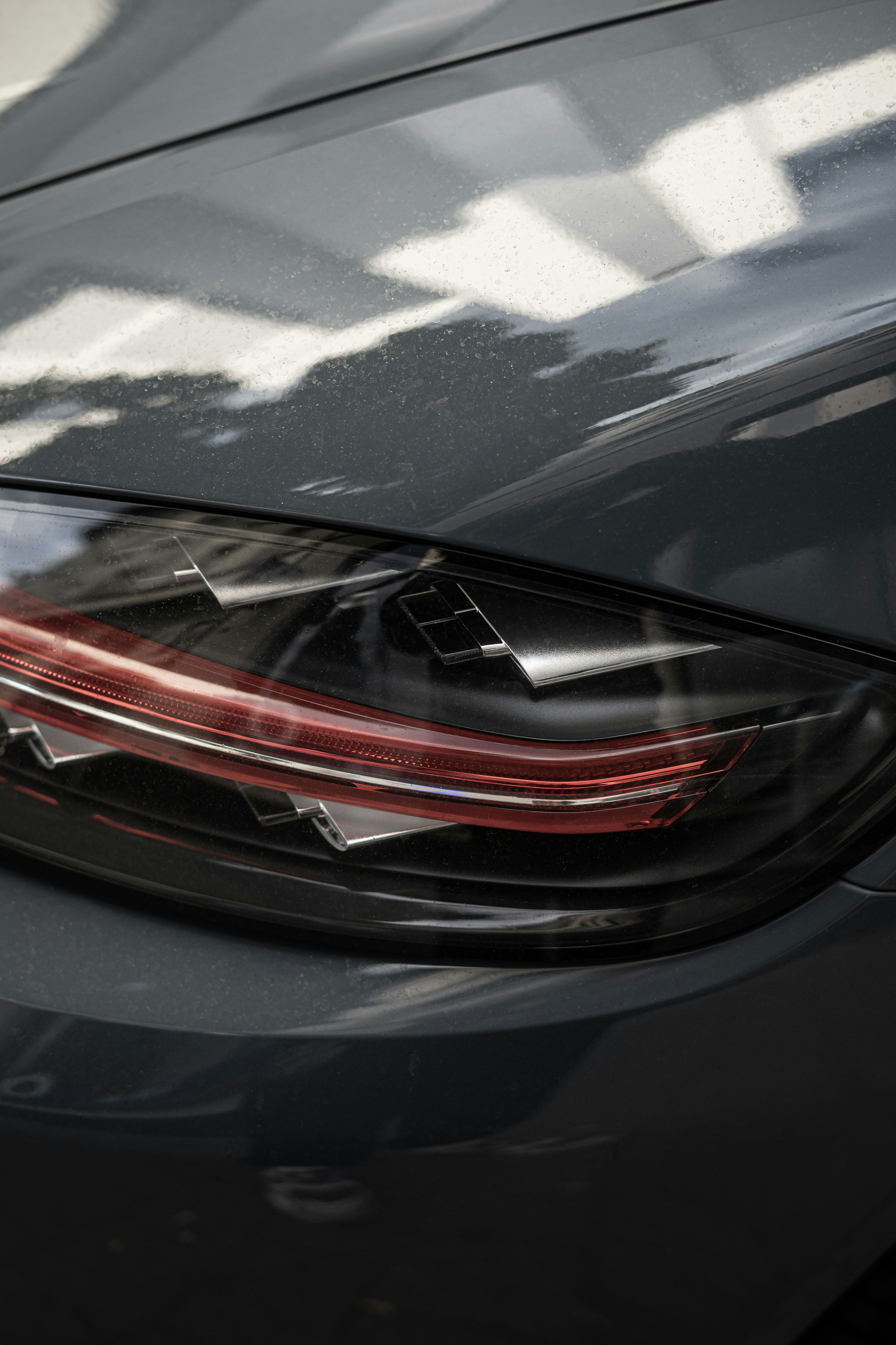 Close-up of a sleek car tail light, showcasing intricate design elements and reflections from surrounding surfaces.
