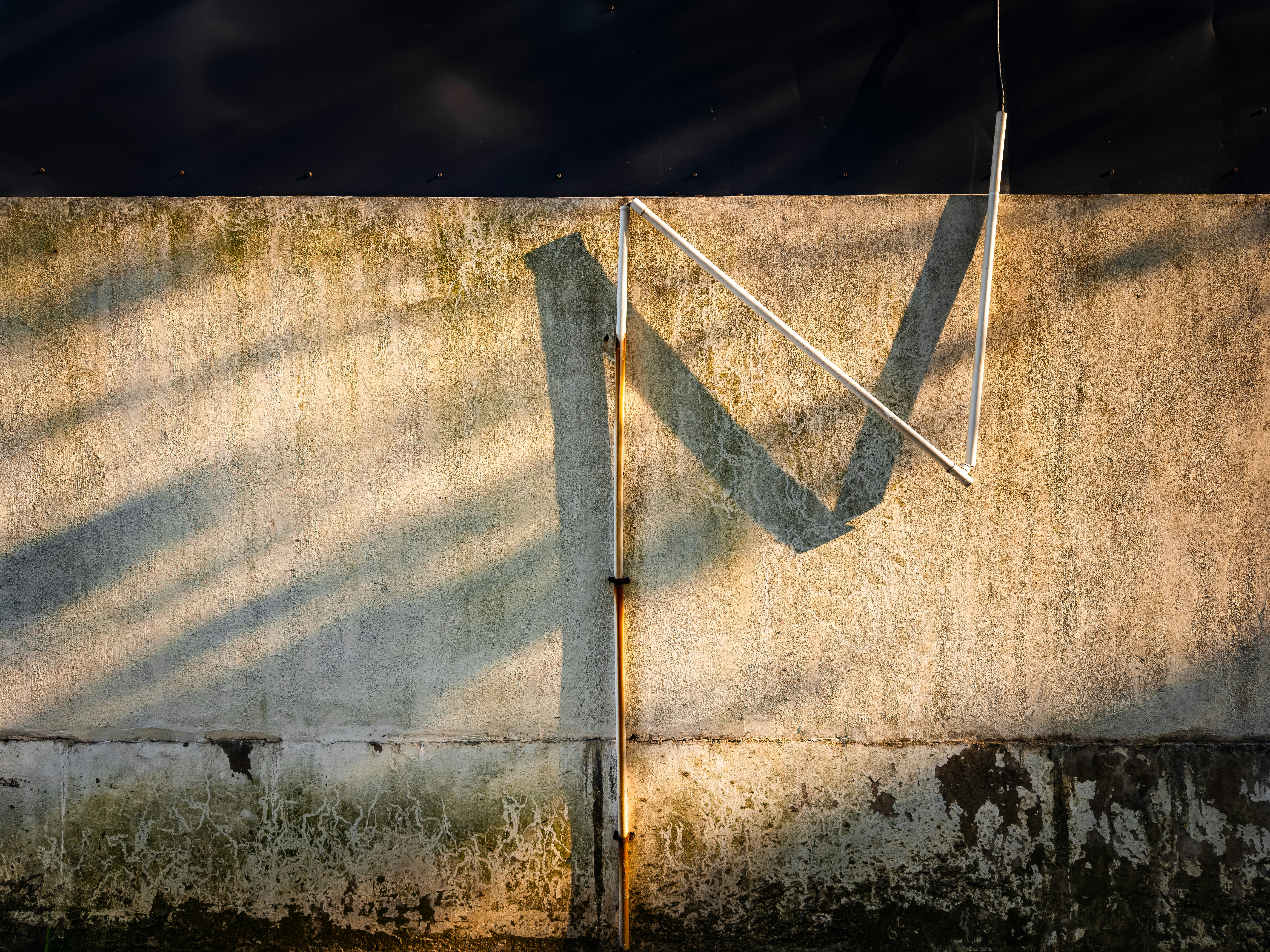 Sunlit Rust and Angular Rails on a Weathered Concrete Wall
