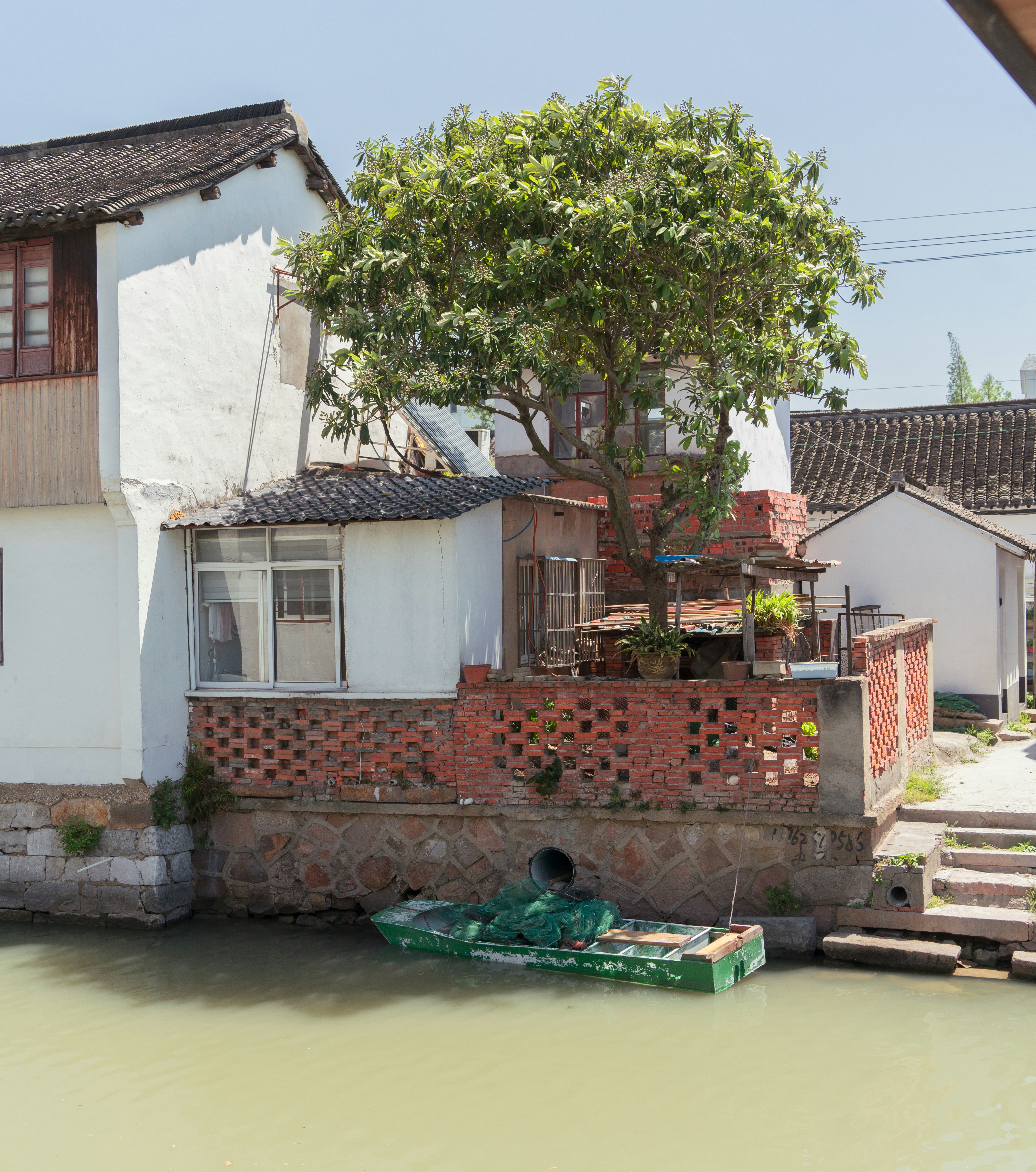 Canalside Oasis: Brick Terrace Beneath a Lush Canopy and a Green Boat