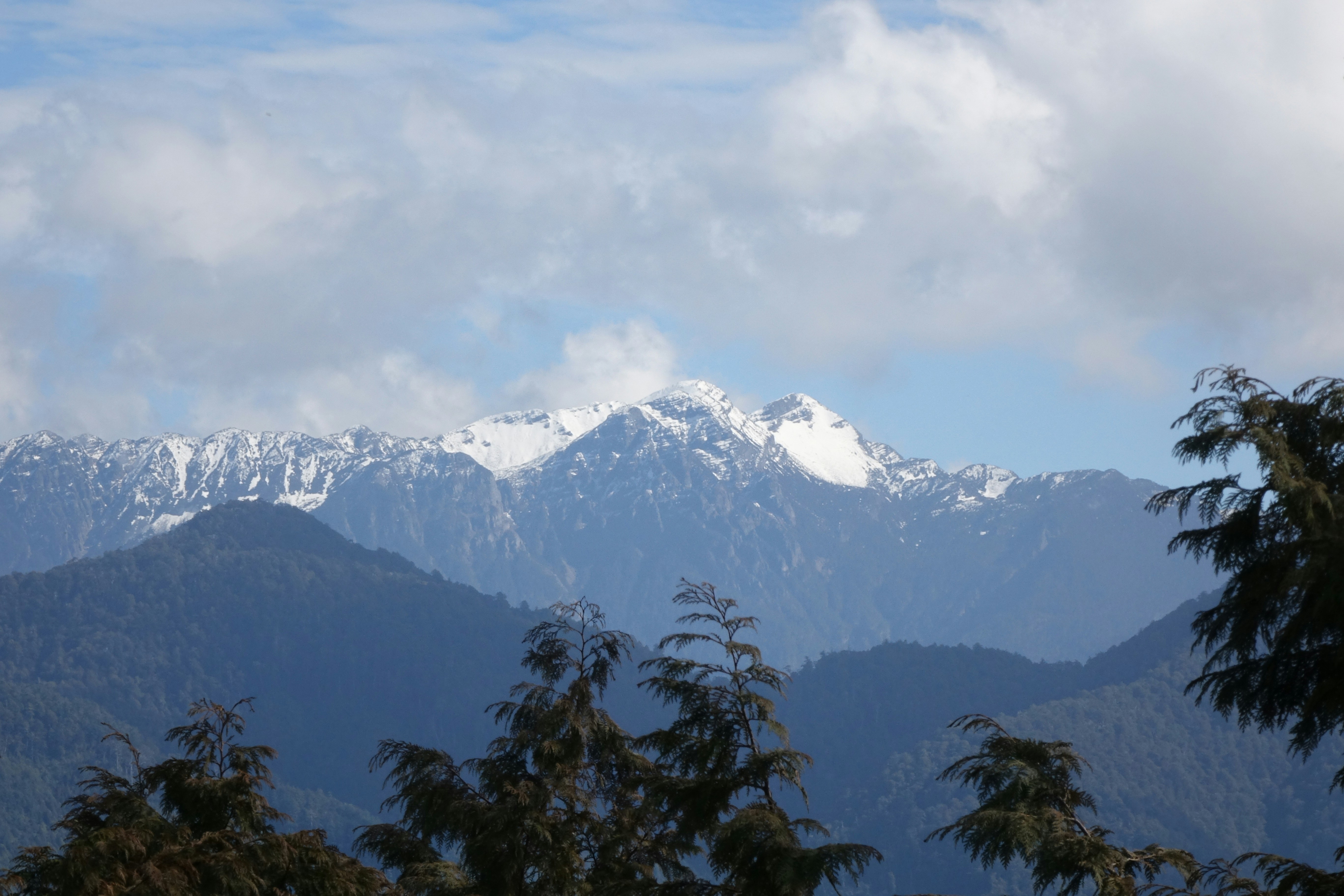 Snow-capped mountains rise above a forested landscape. photo – Free ...