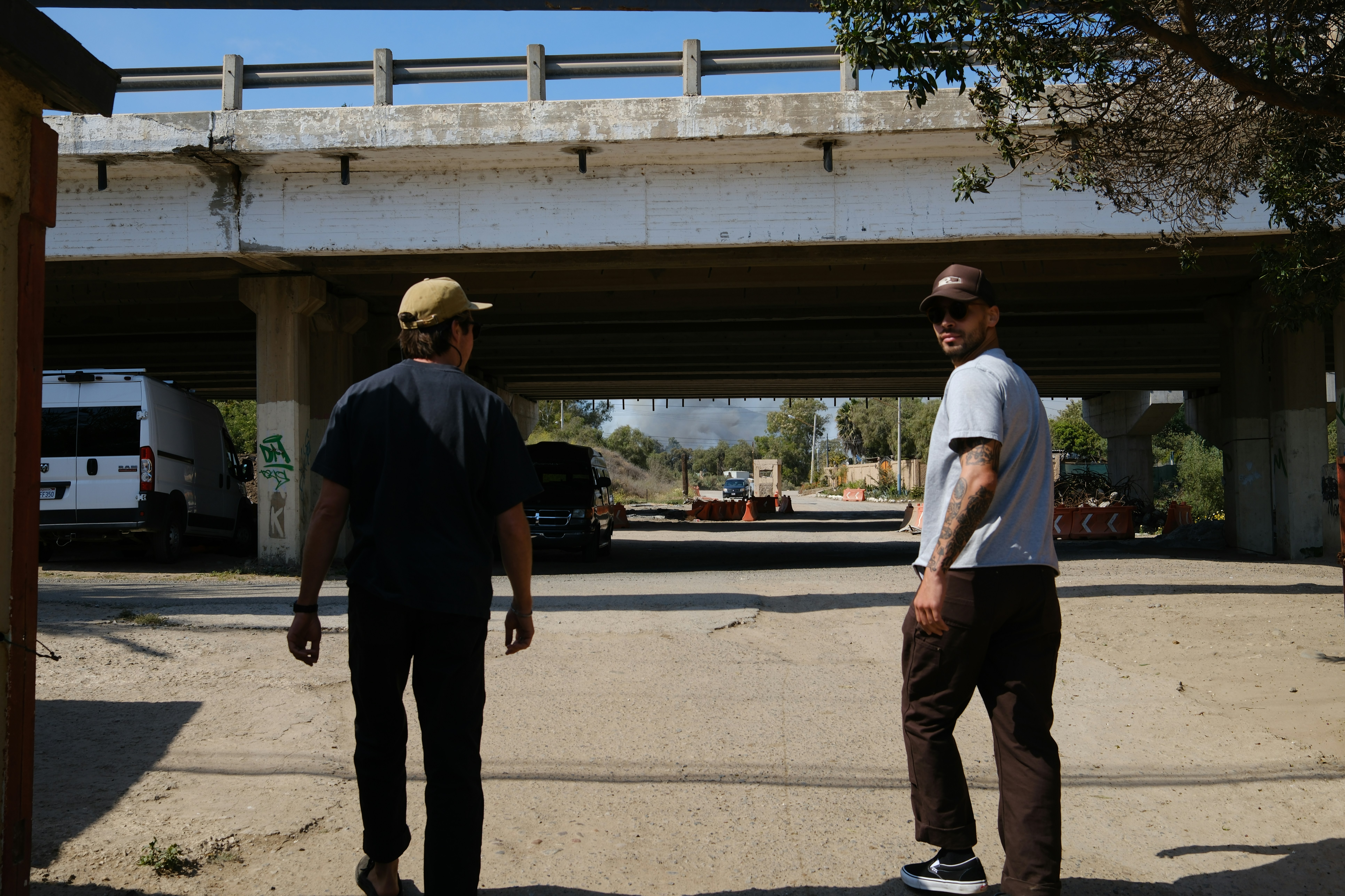 Grounded in Sunlight: Two Men Under a Weathered Overpass