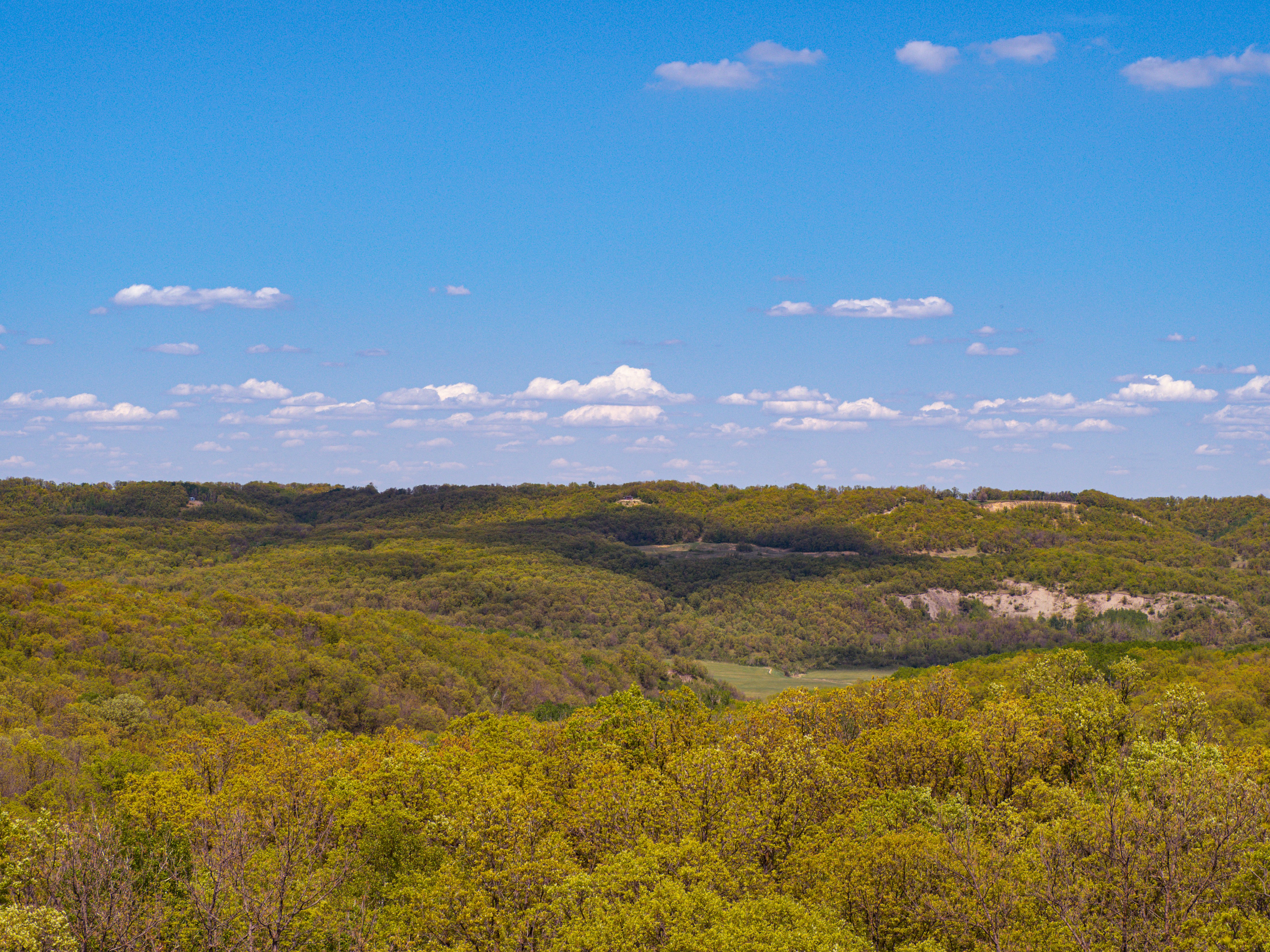 Lush green hills stretch across the valley under a clear blue sky dotted with fluffy clouds.