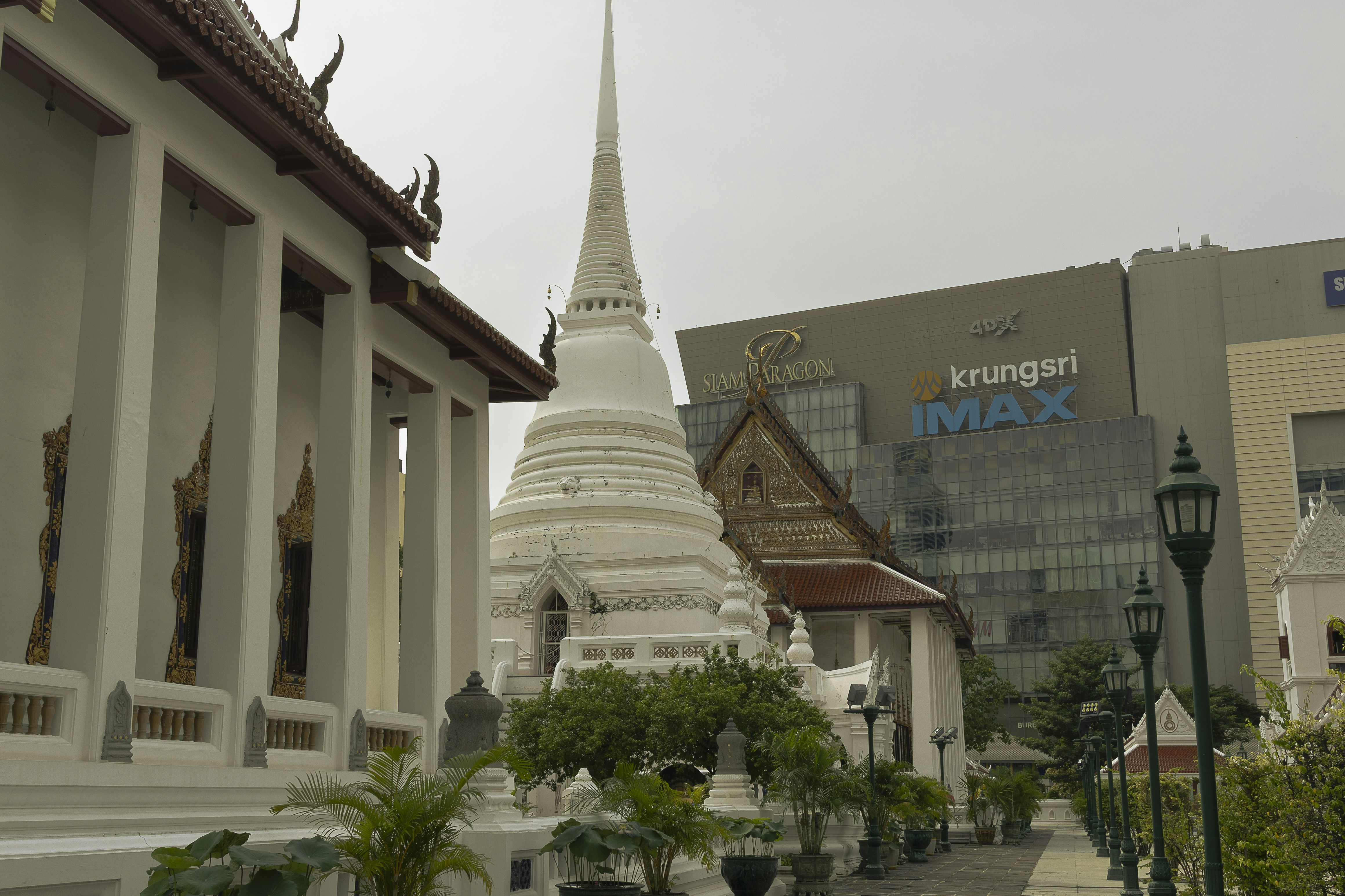 Intricate white stupa juxtaposed against a modern commercial building, showcasing a blend of cultural heritage and contemporary architecture.