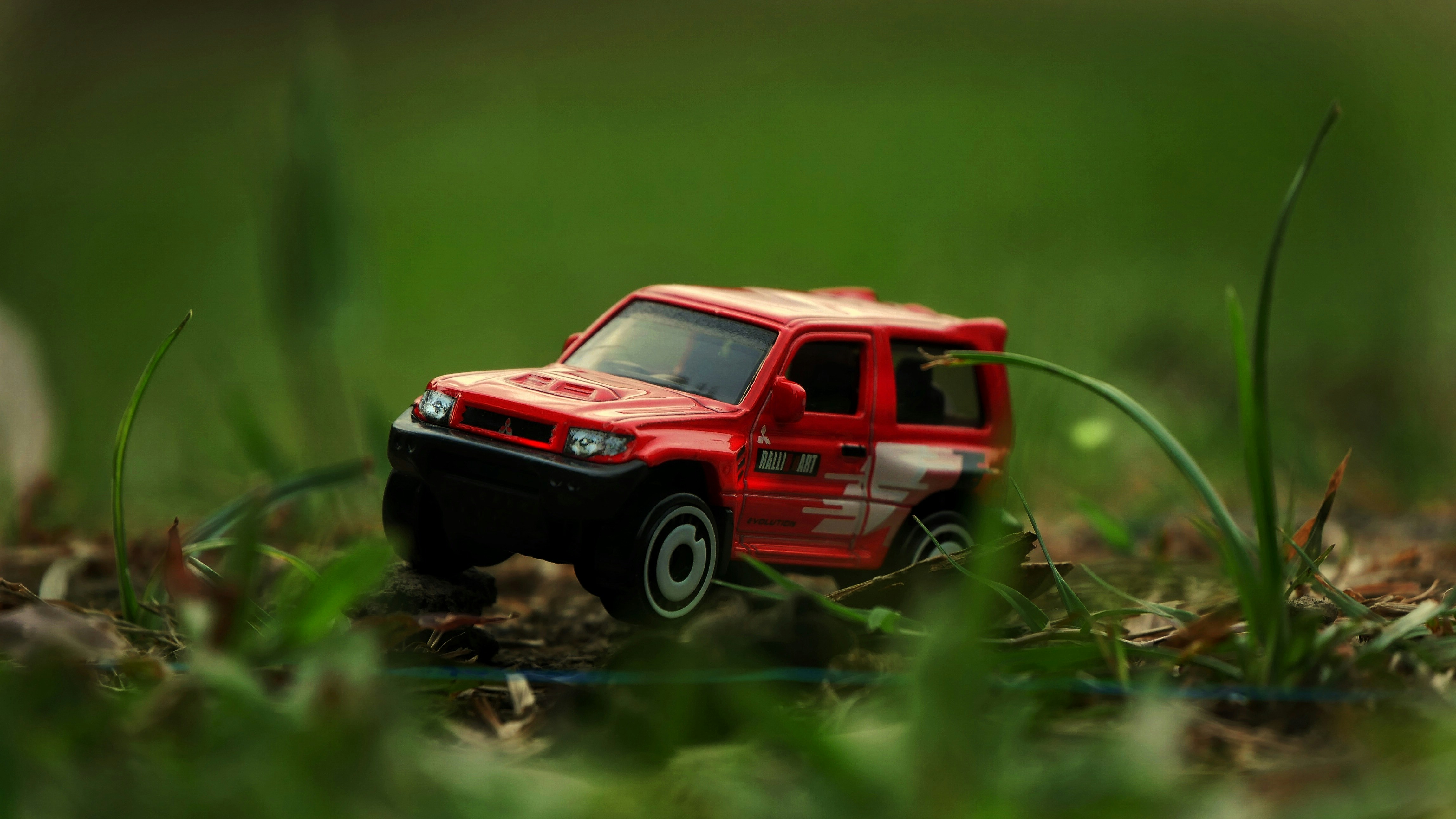 Crimson Micro-Terrain: A Toy SUV Navigates Leaf-Littered Ground in a Backyard Landscape