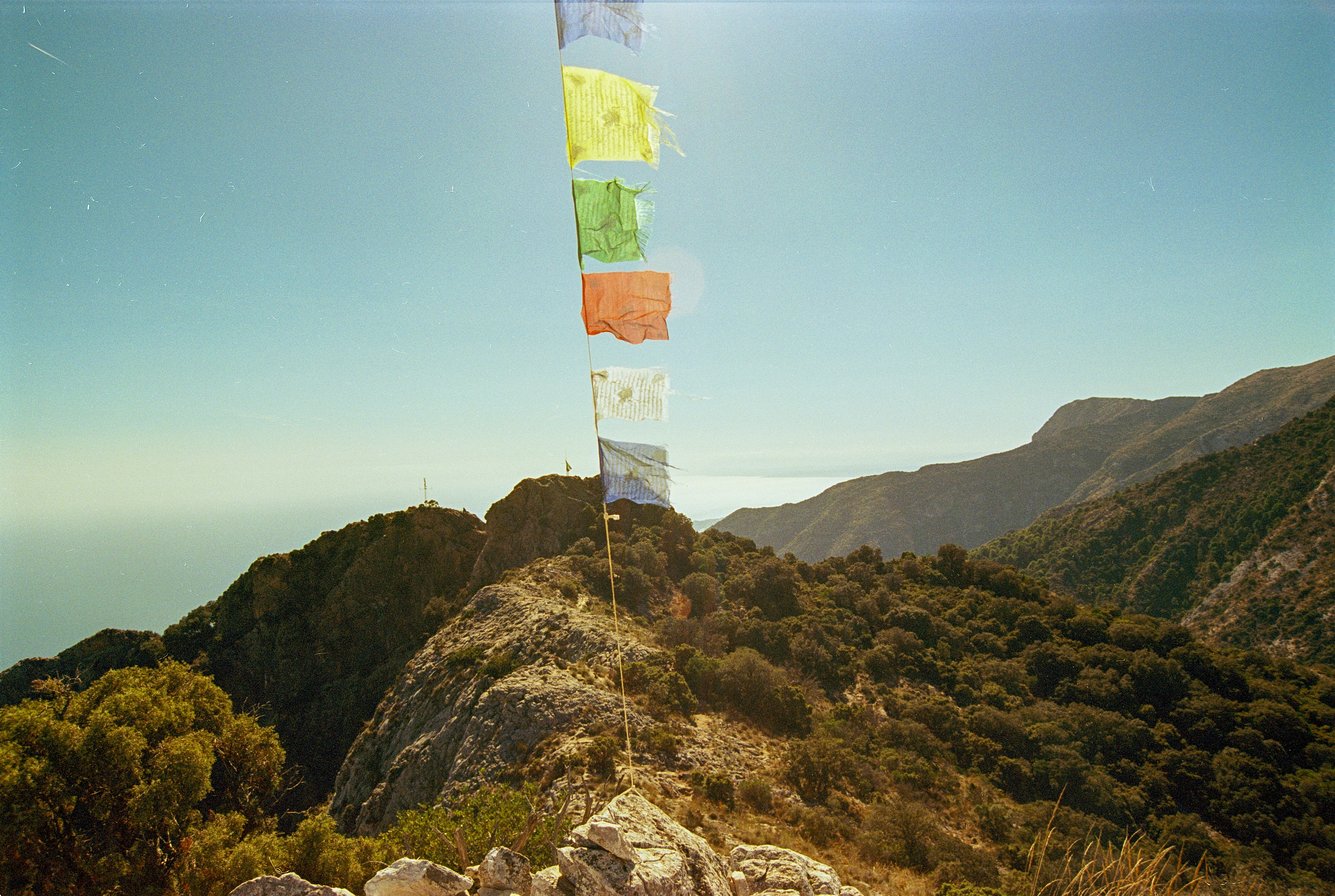 Colorful flags flutter on a mountain's peak.