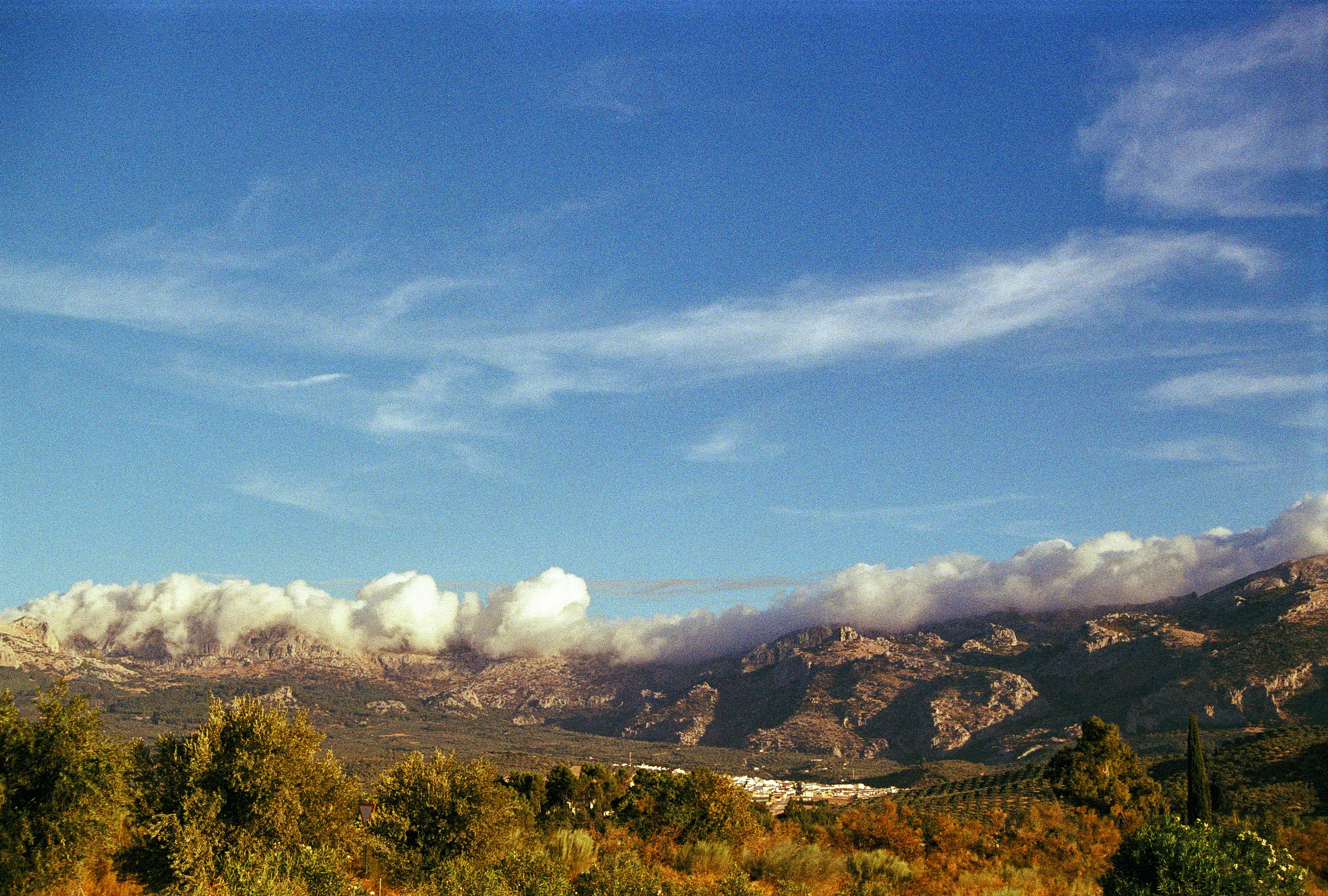 Lush green landscape with rolling hills and dramatic cloud formations above a distant mountain range.